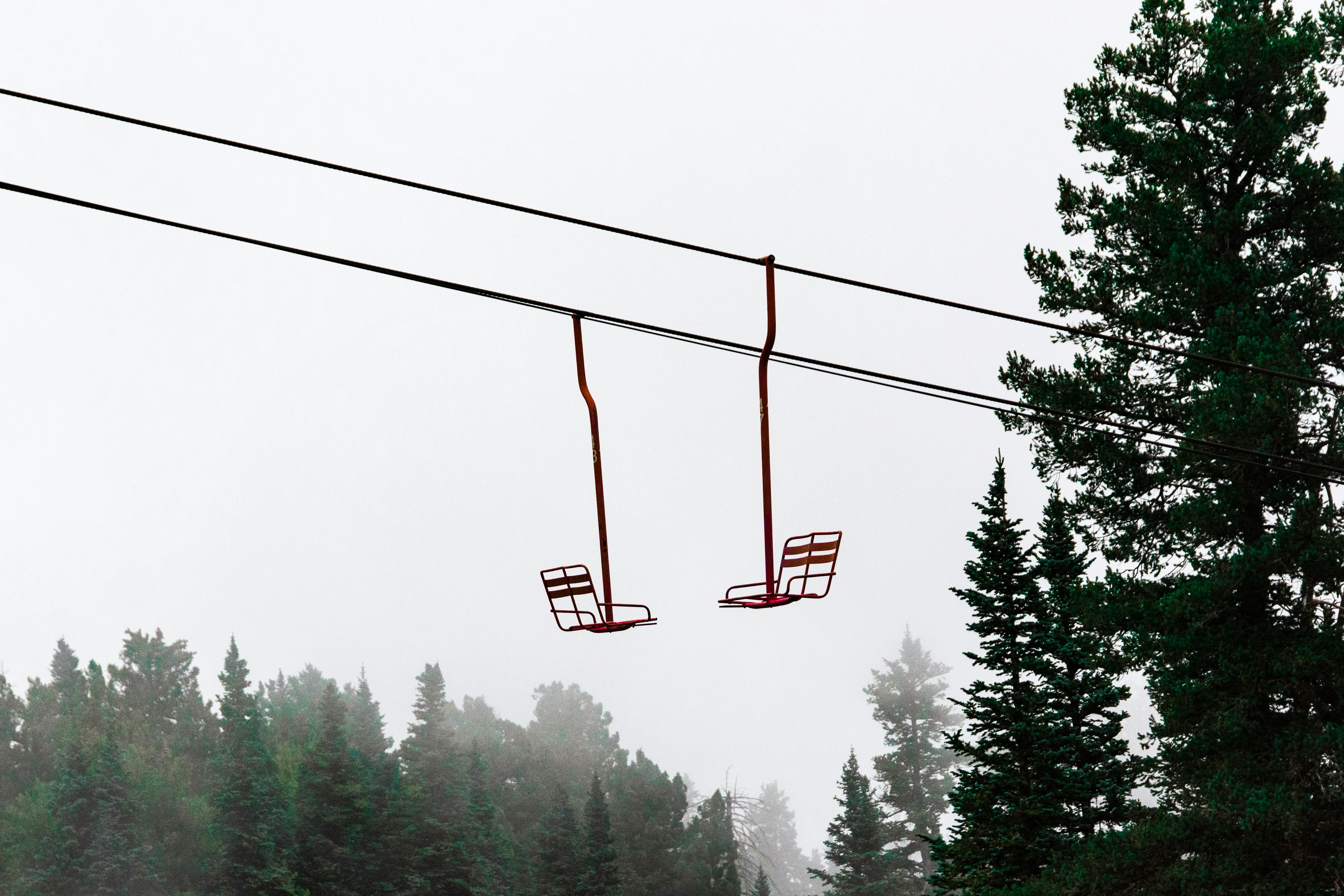 Two empty ski lift chairs suspended above a dense forest, enveloped in fog. The scene evokes a sense of solitude and nostalgia.