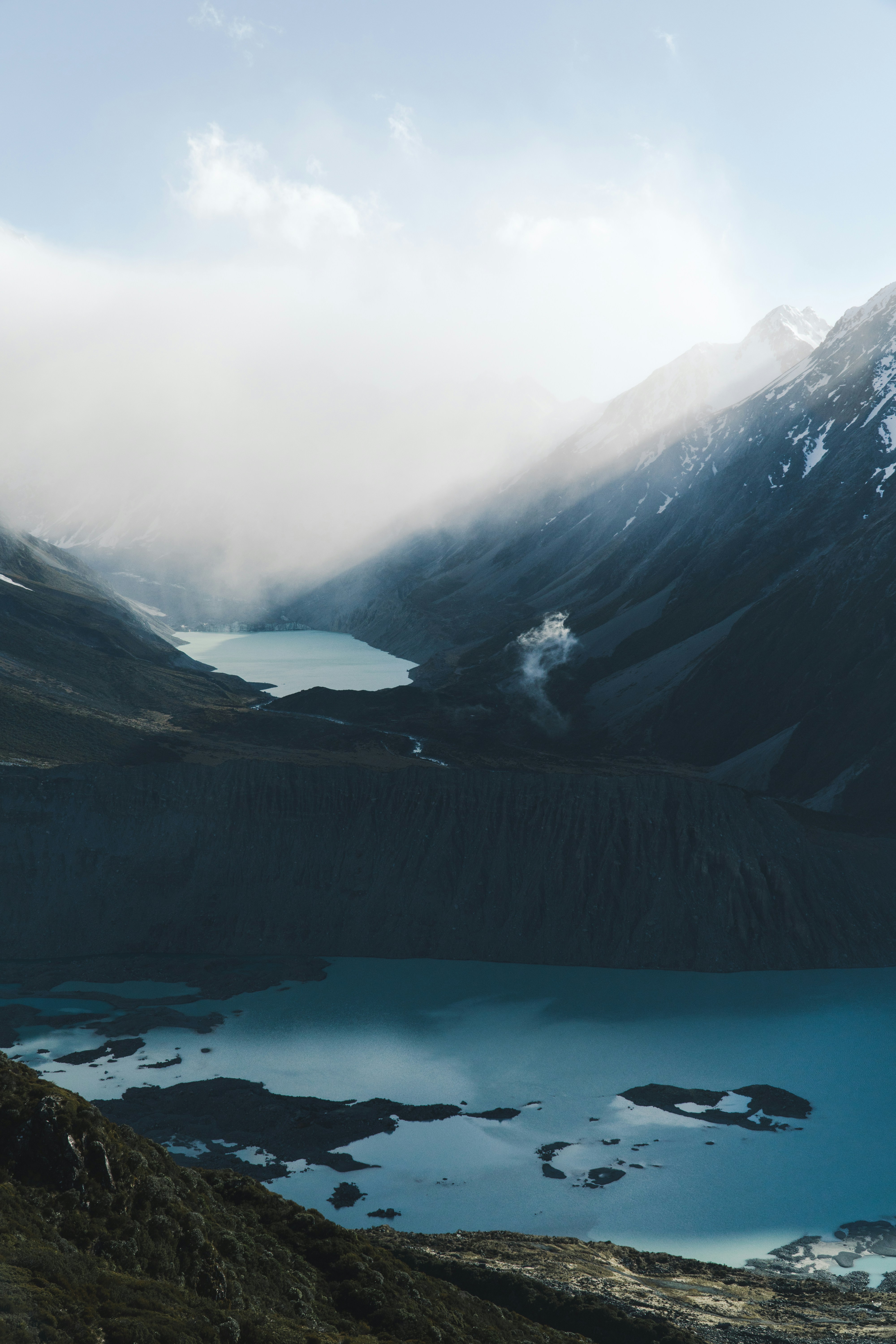 Morning mist drifts over serene mountain lakes in Mt Cook National Park, framed by rugged peaks.