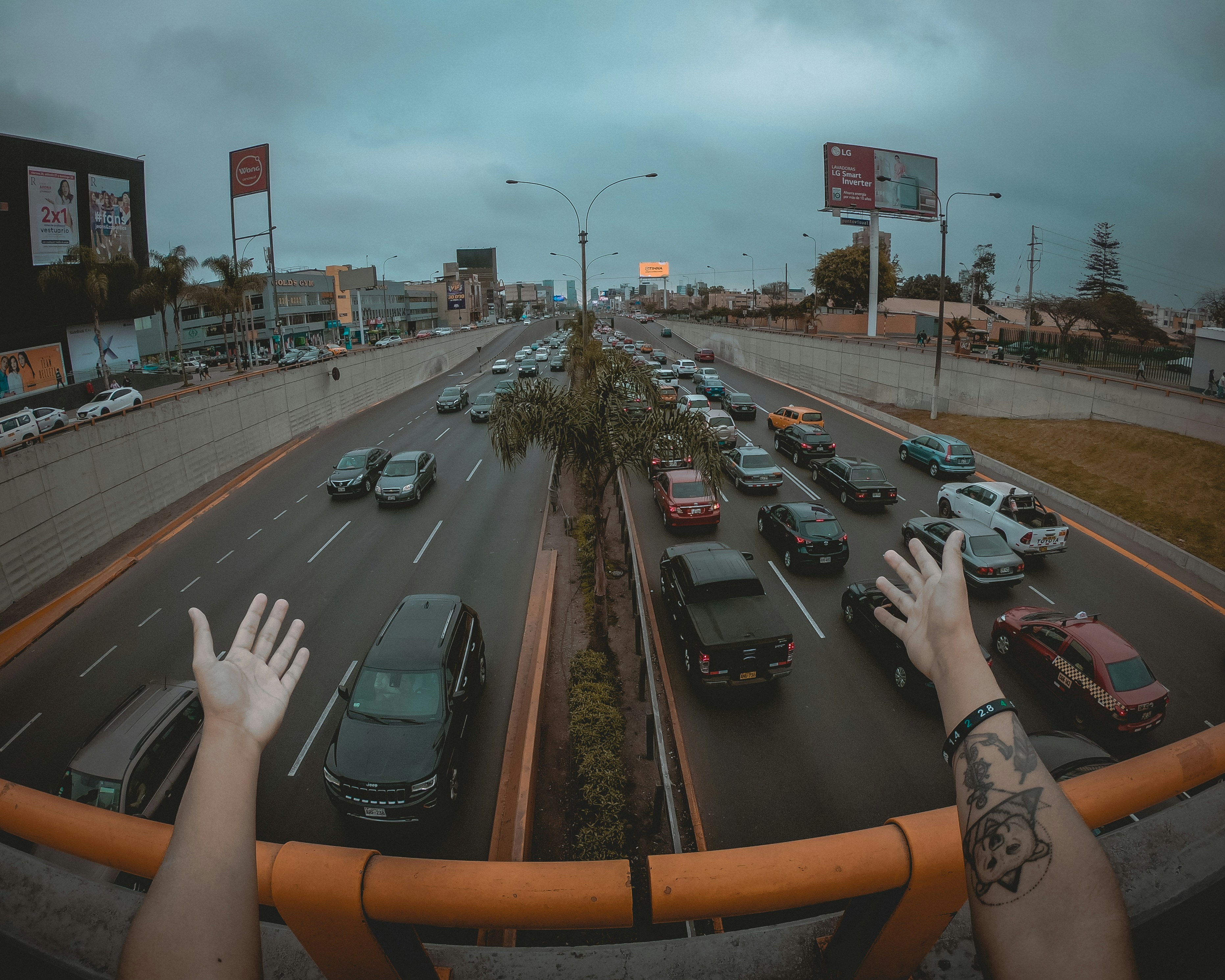 Hands reaching out from a bridge above a bustling highway, capturing the energy of city life during twilight.