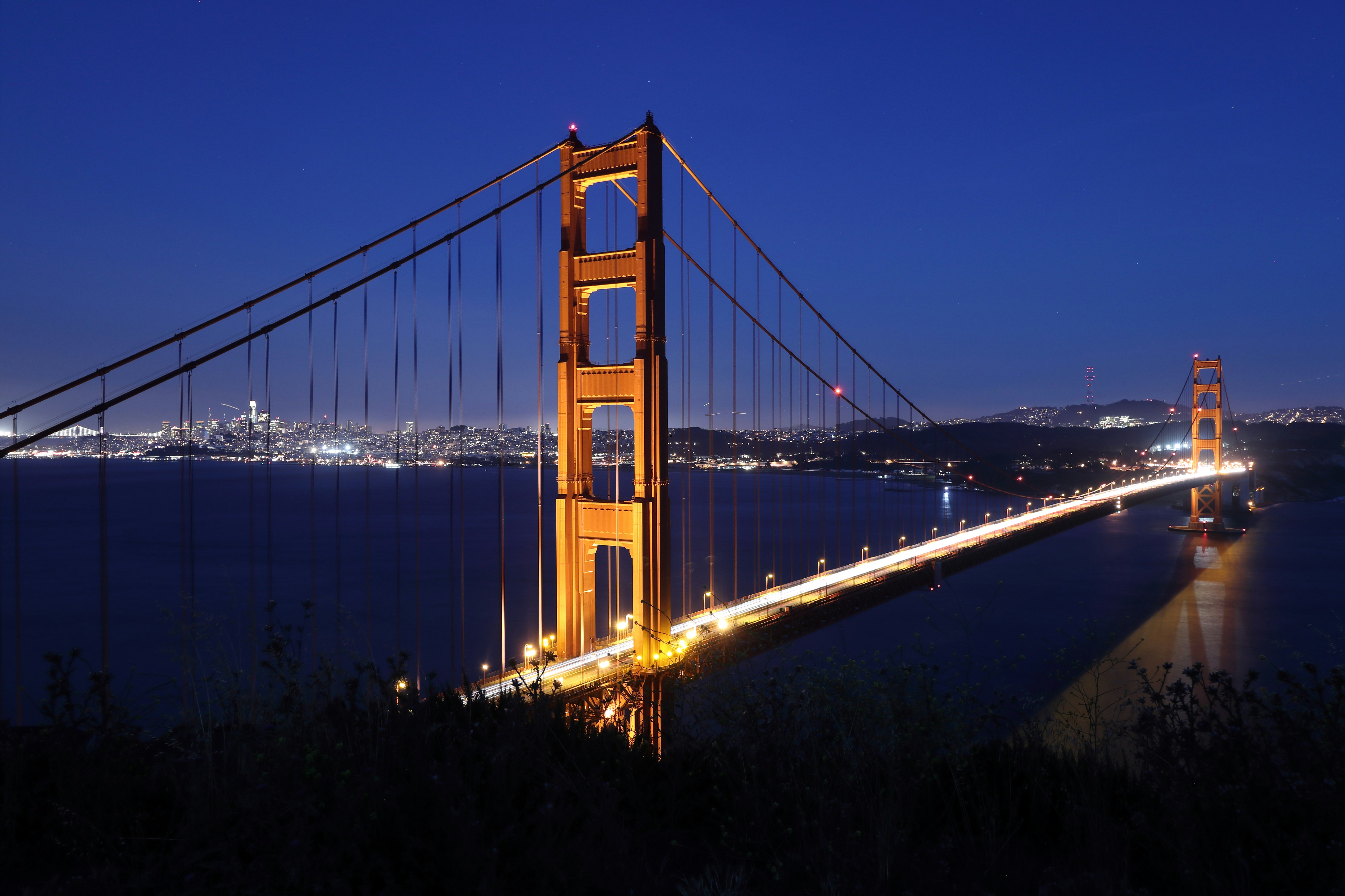 Golden Gate Bridge glowing under a deep blue night sky with city lights in the background.