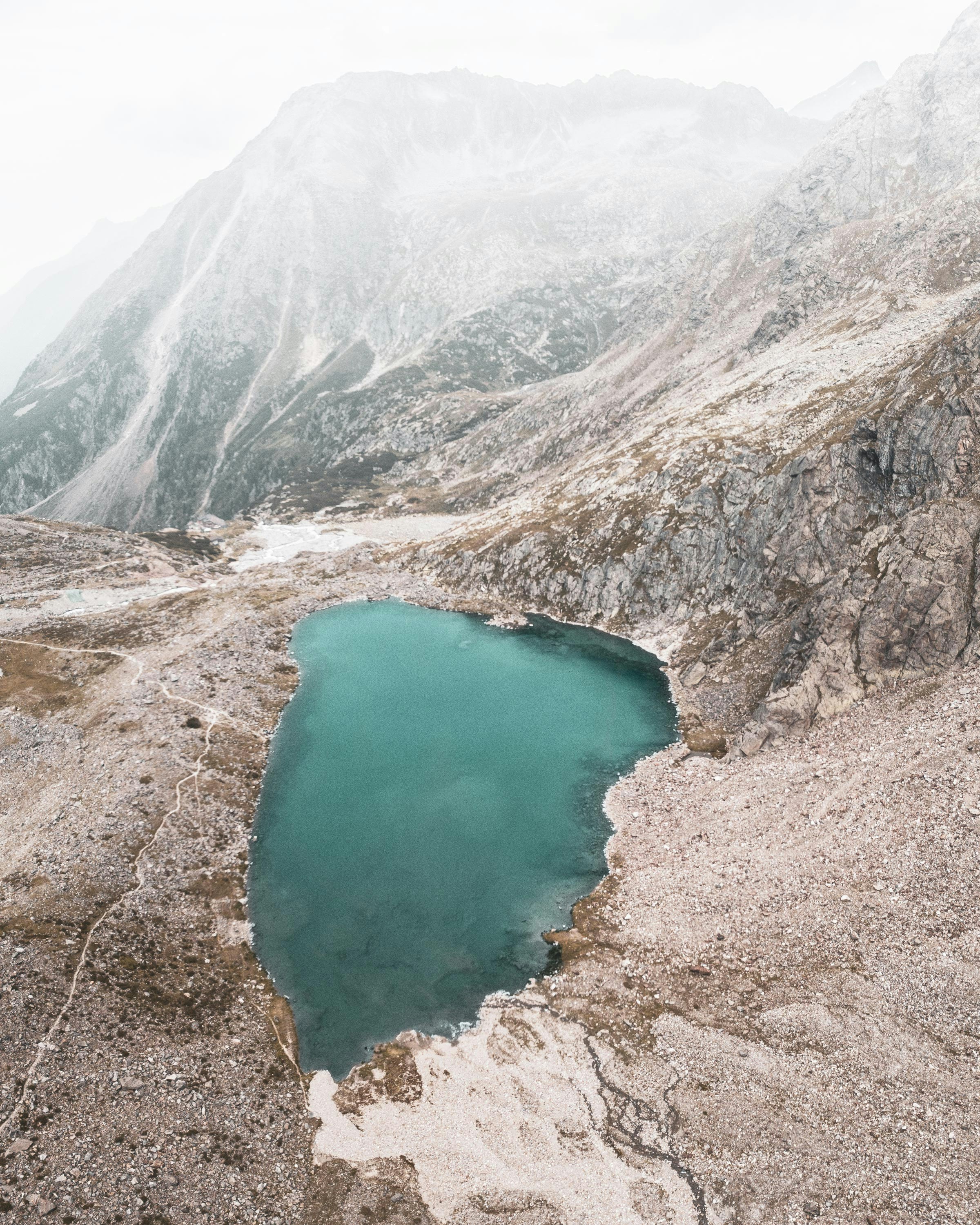 Aerial view of a turquoise lake nestled in rocky mountain terrain under a misty sky.
