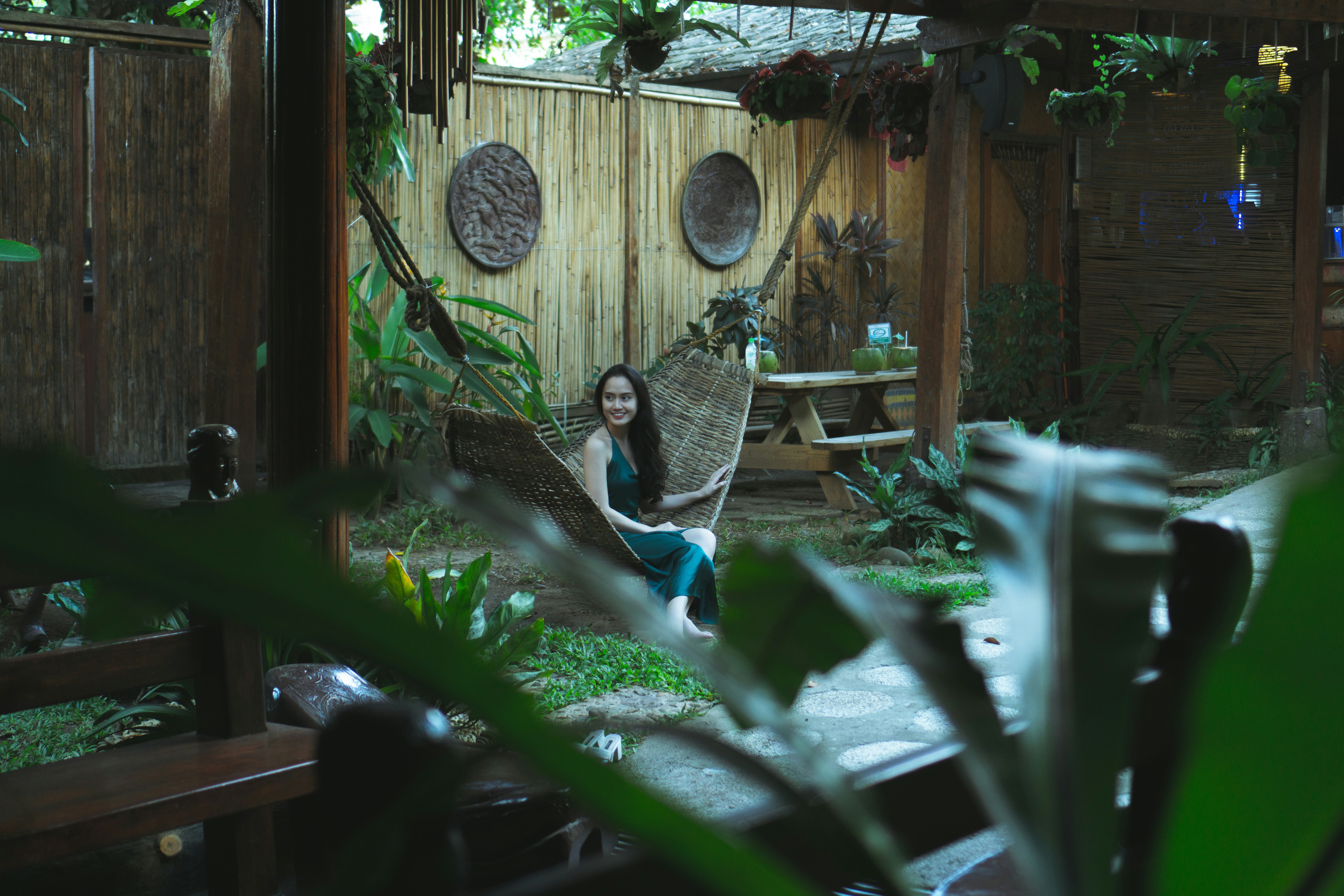 Woman sitting on a hammock in a serene, plant-filled patio.
