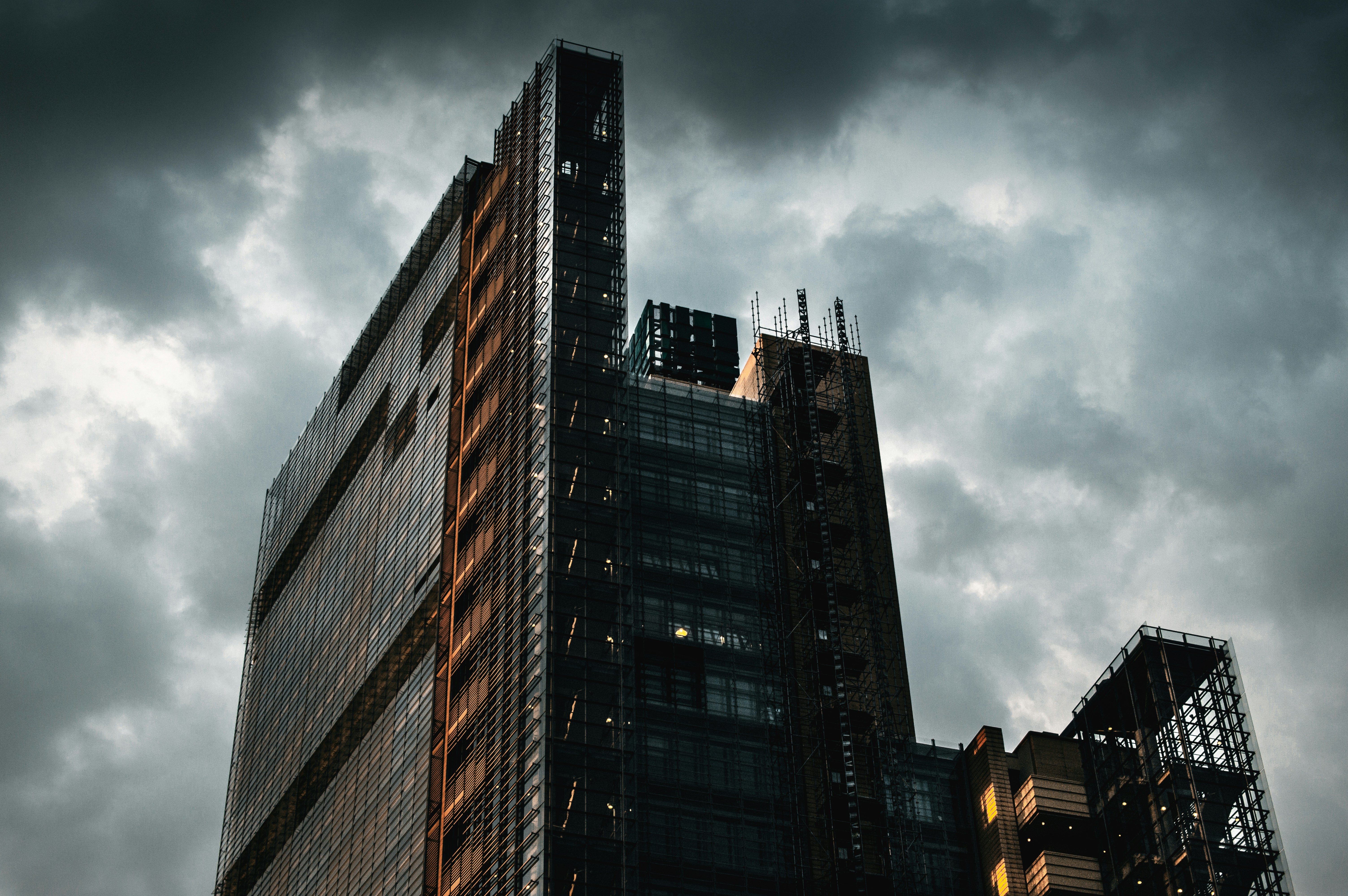Towering skyscraper with reflective glass facade against a backdrop of dramatic clouds.