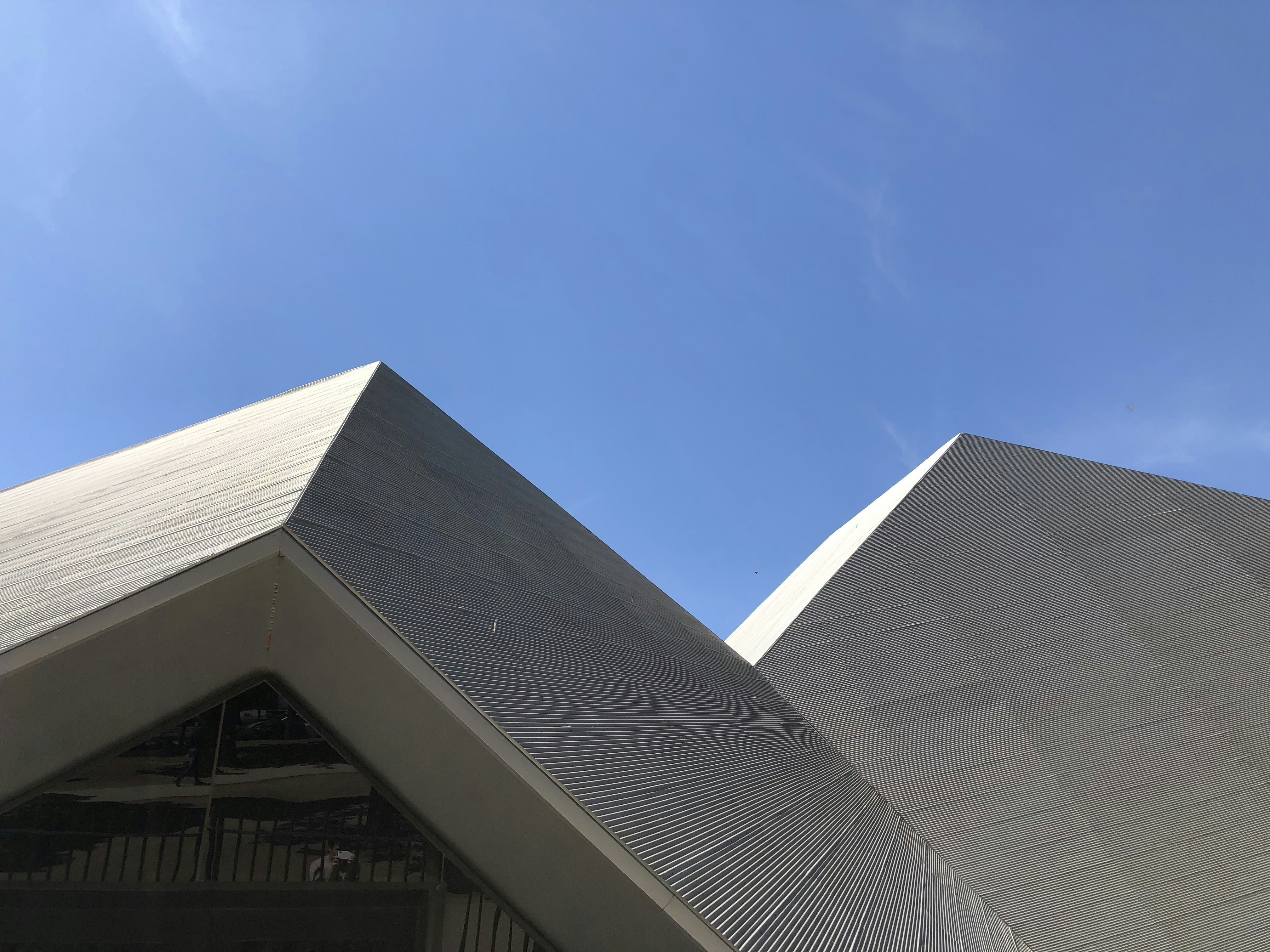 Two sharply angled rooftops converge under a clear blue sky, showcasing modern architectural design.