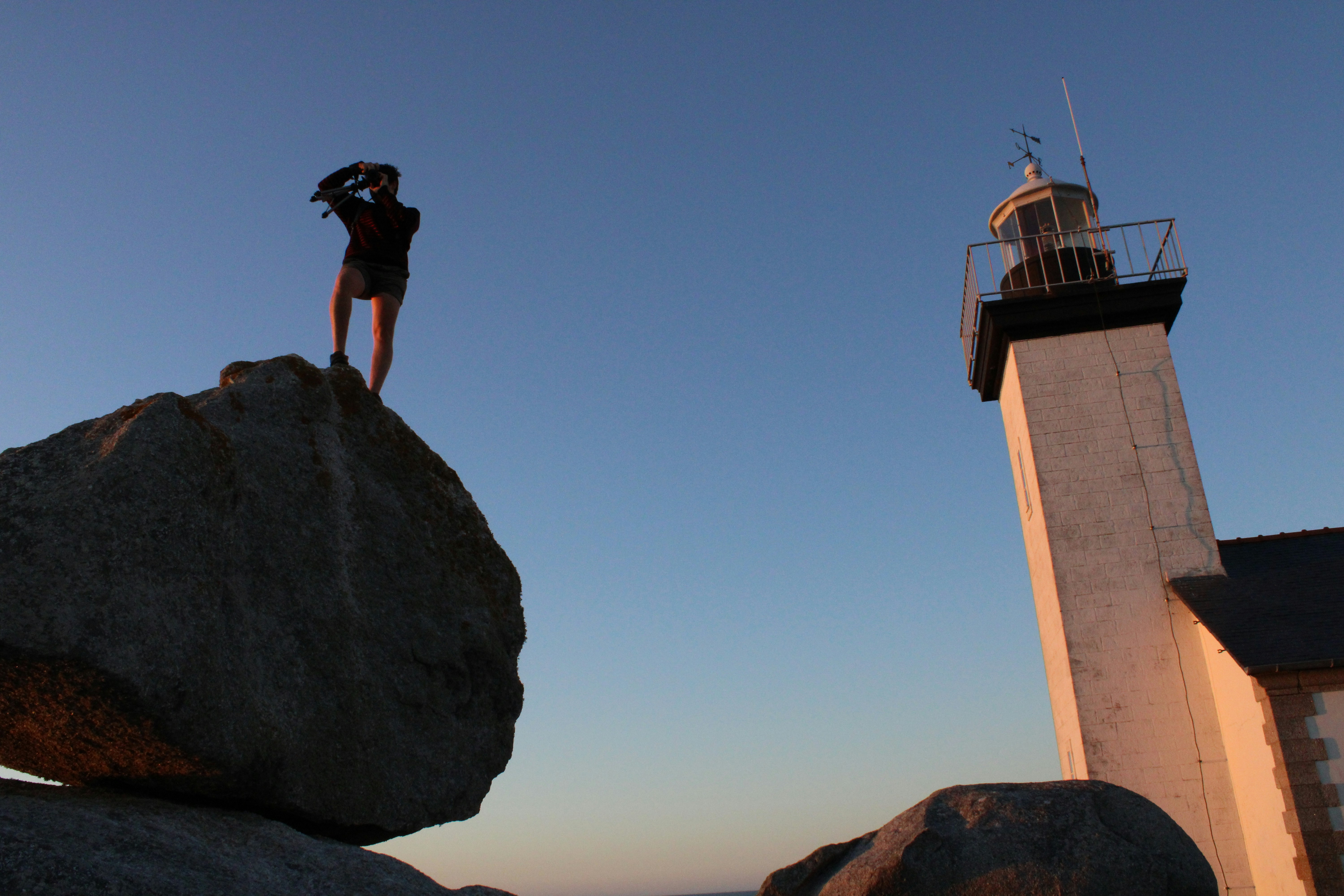 Dusk Sentinel: climber perched on granite beside a lighthouse