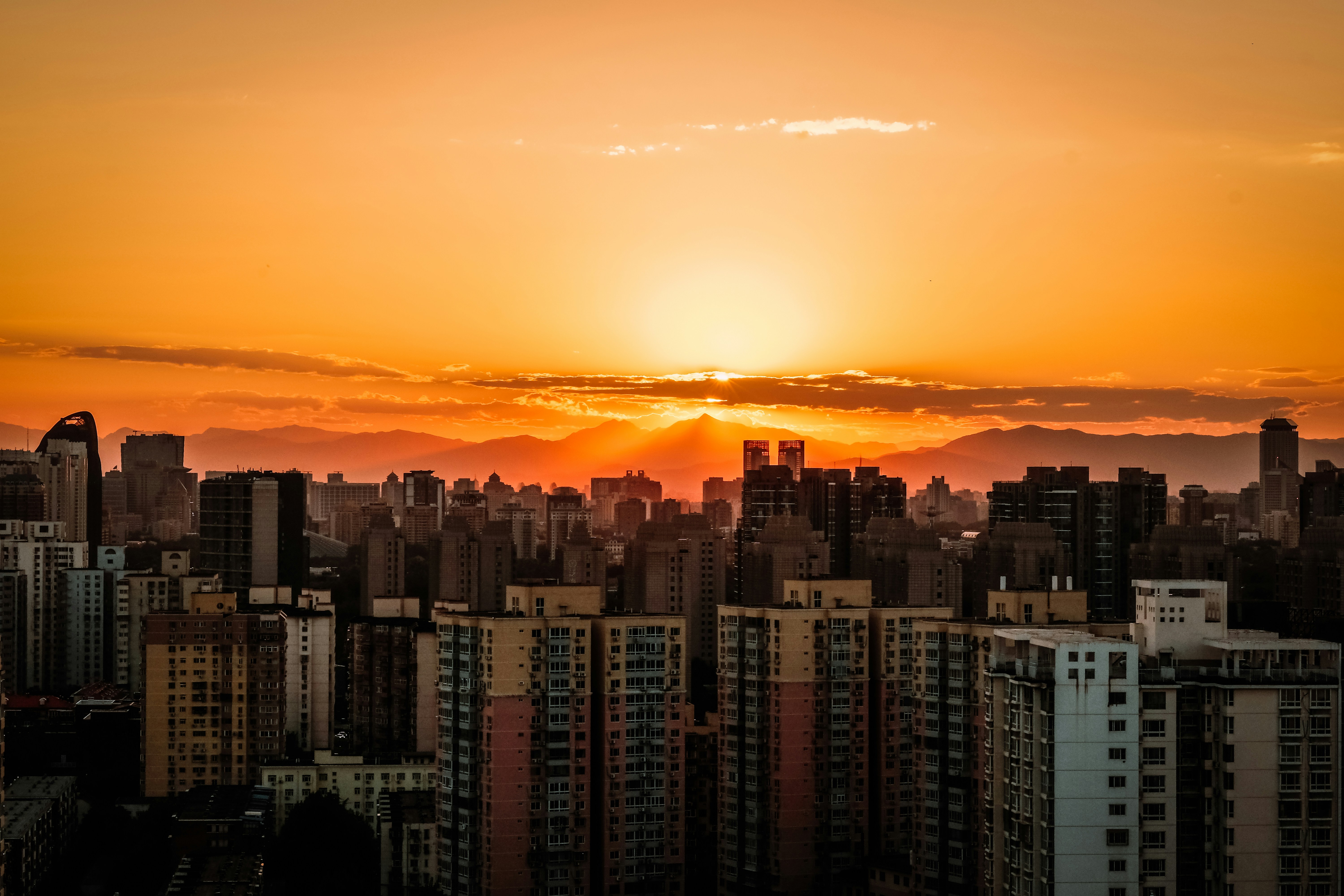 Sunset over Beijing skyline with silhouetted buildings against an orange sky.