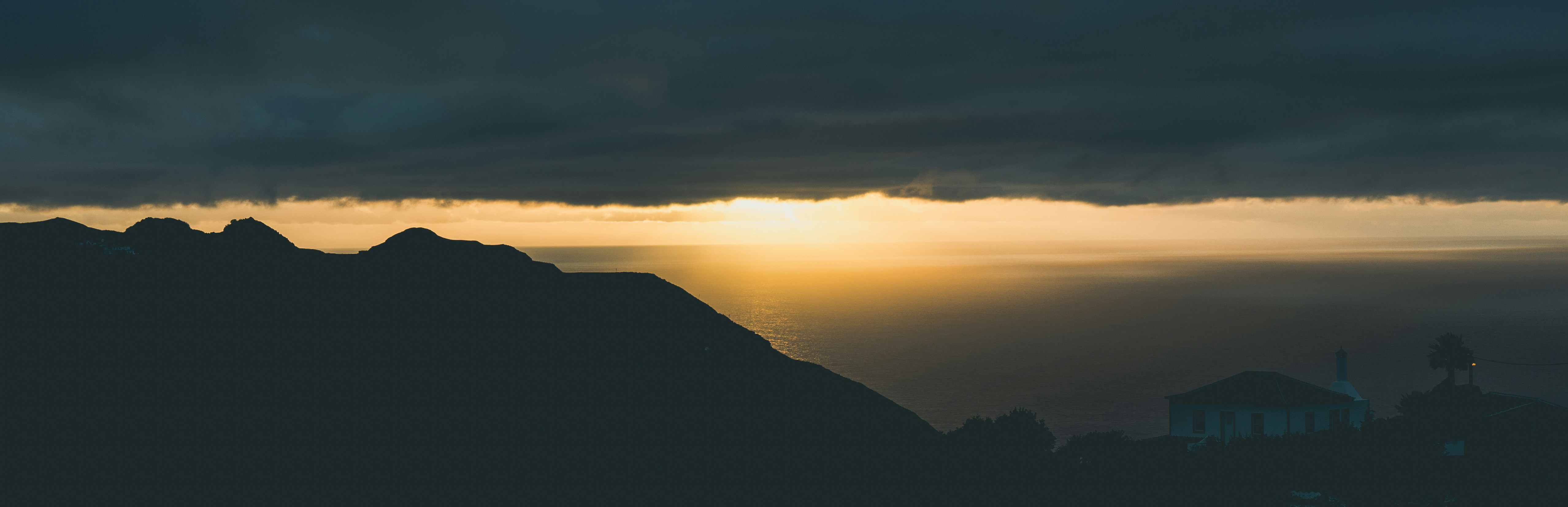Golden sunrise peeks through dark clouds above the silhouette of Santa Maria's rugged landscape.