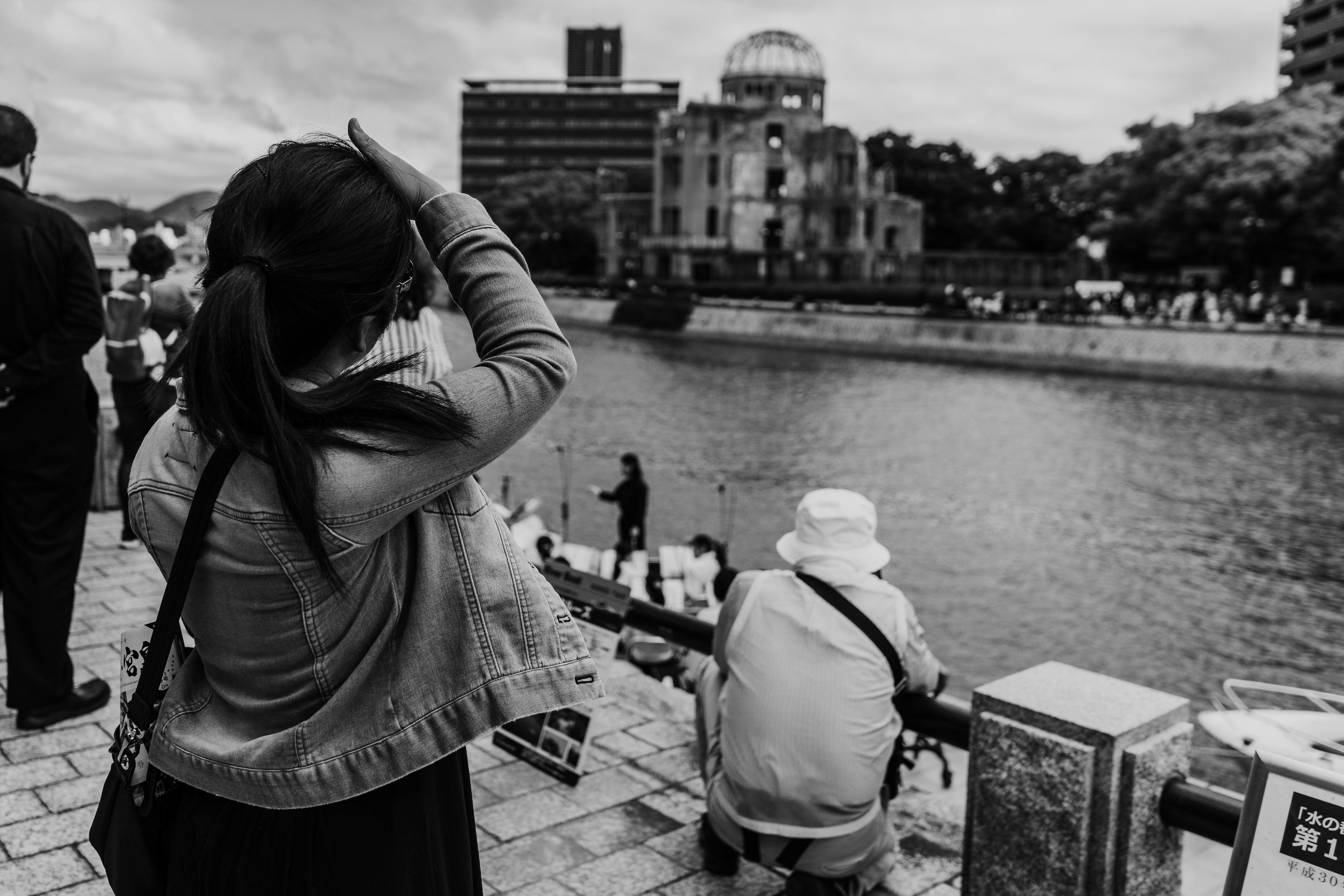 Grayscale scene of people observing a river with a historic building in the background.