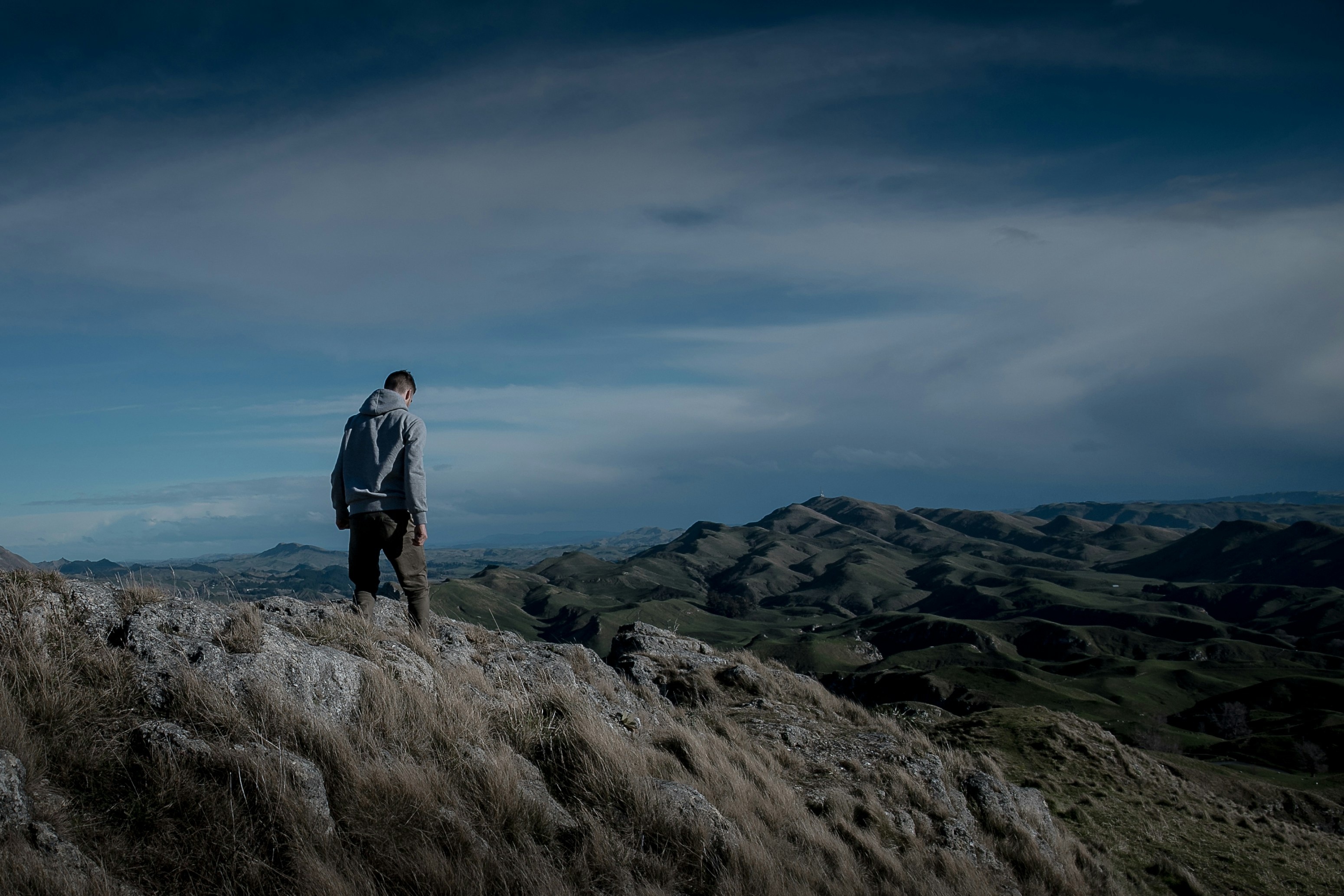 Hiker standing on a rocky hilltop with expansive rolling hills under a dramatic sky.