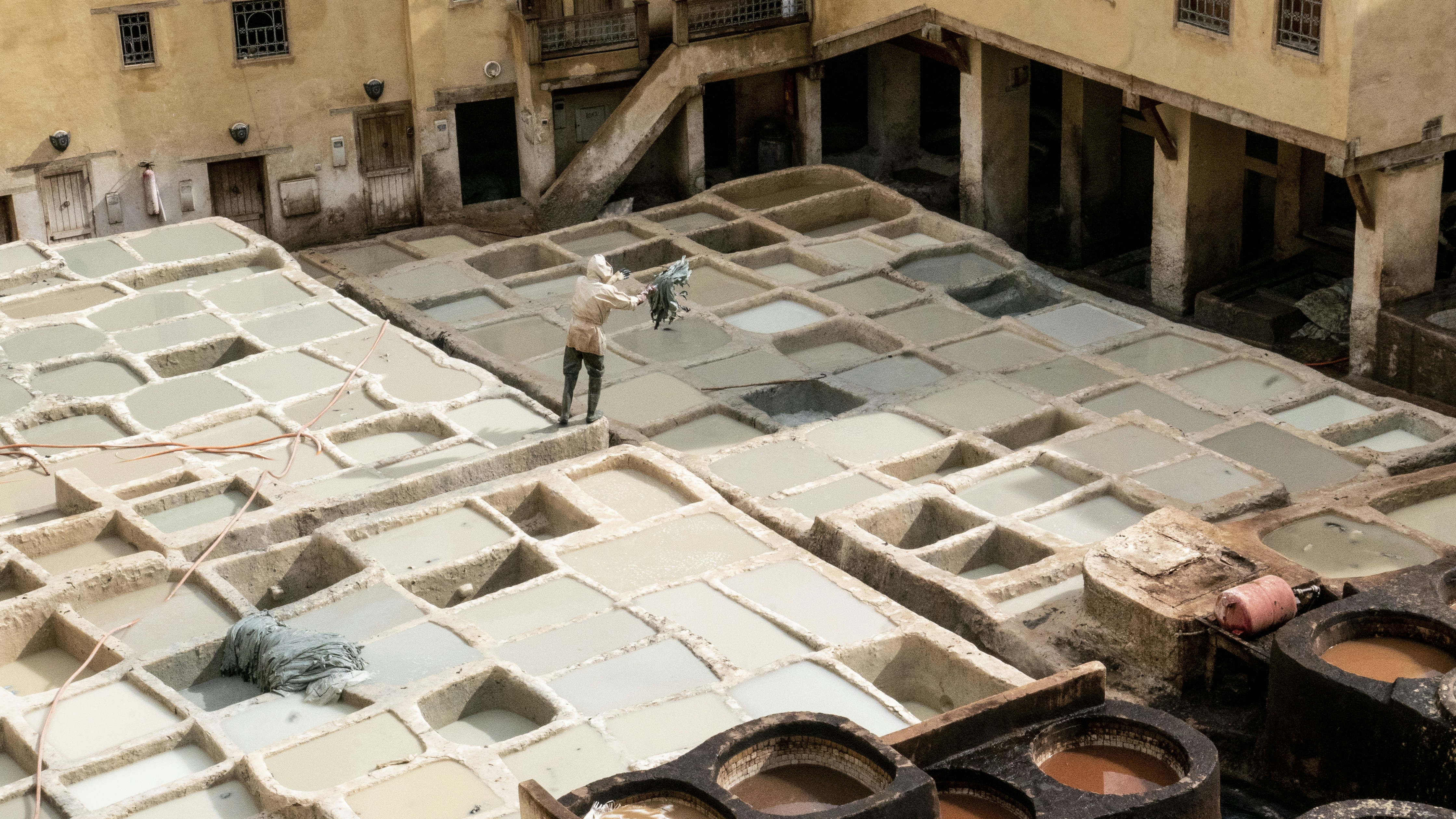 Man standing in a tannery, tossing leather into colorful dye pits surrounded by aged buildings.