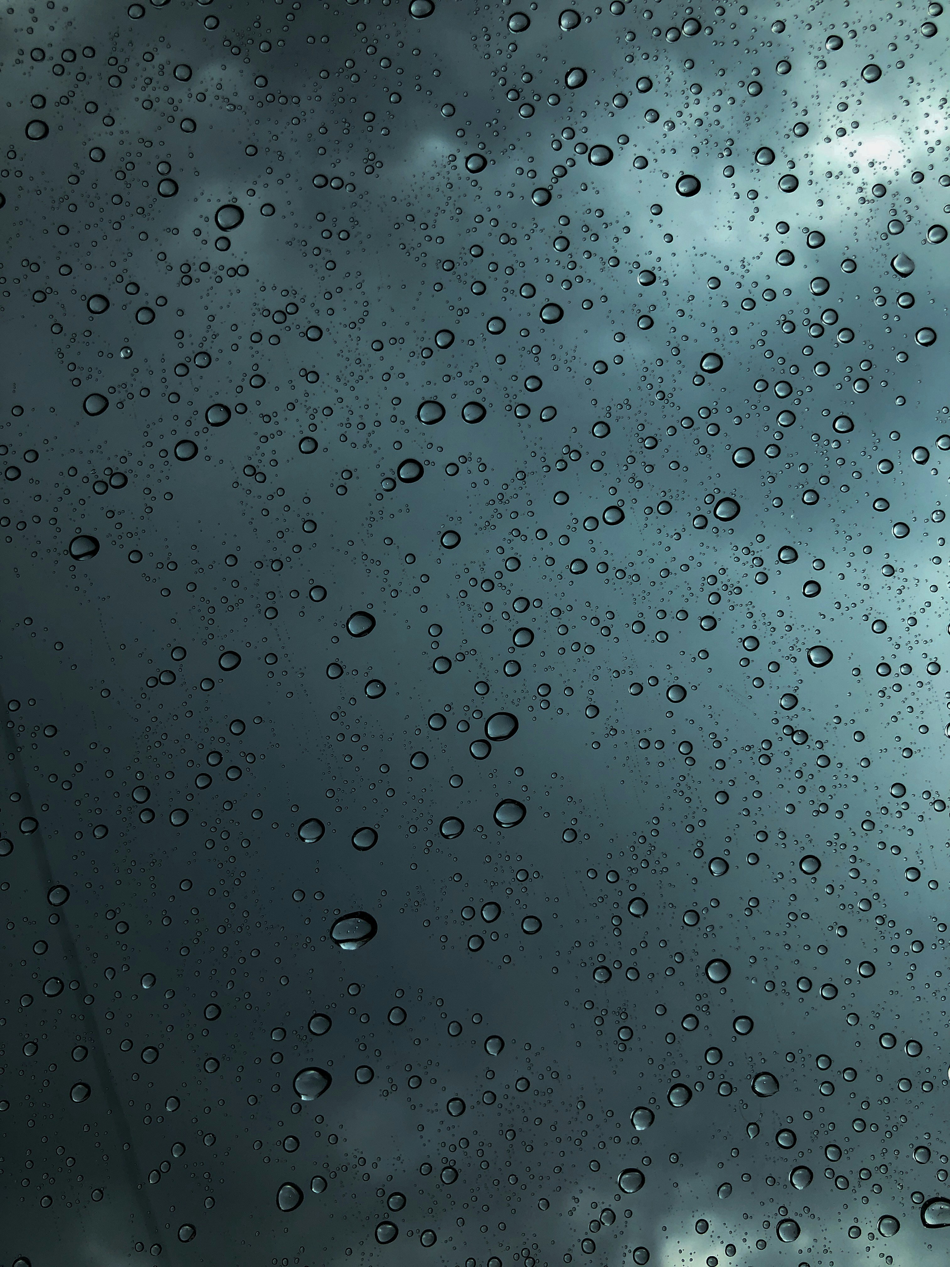 Raindrops cling to a window, creating a textured view of the stormy sky beyond. The interplay of light and water enhances the moody atmosphere.
