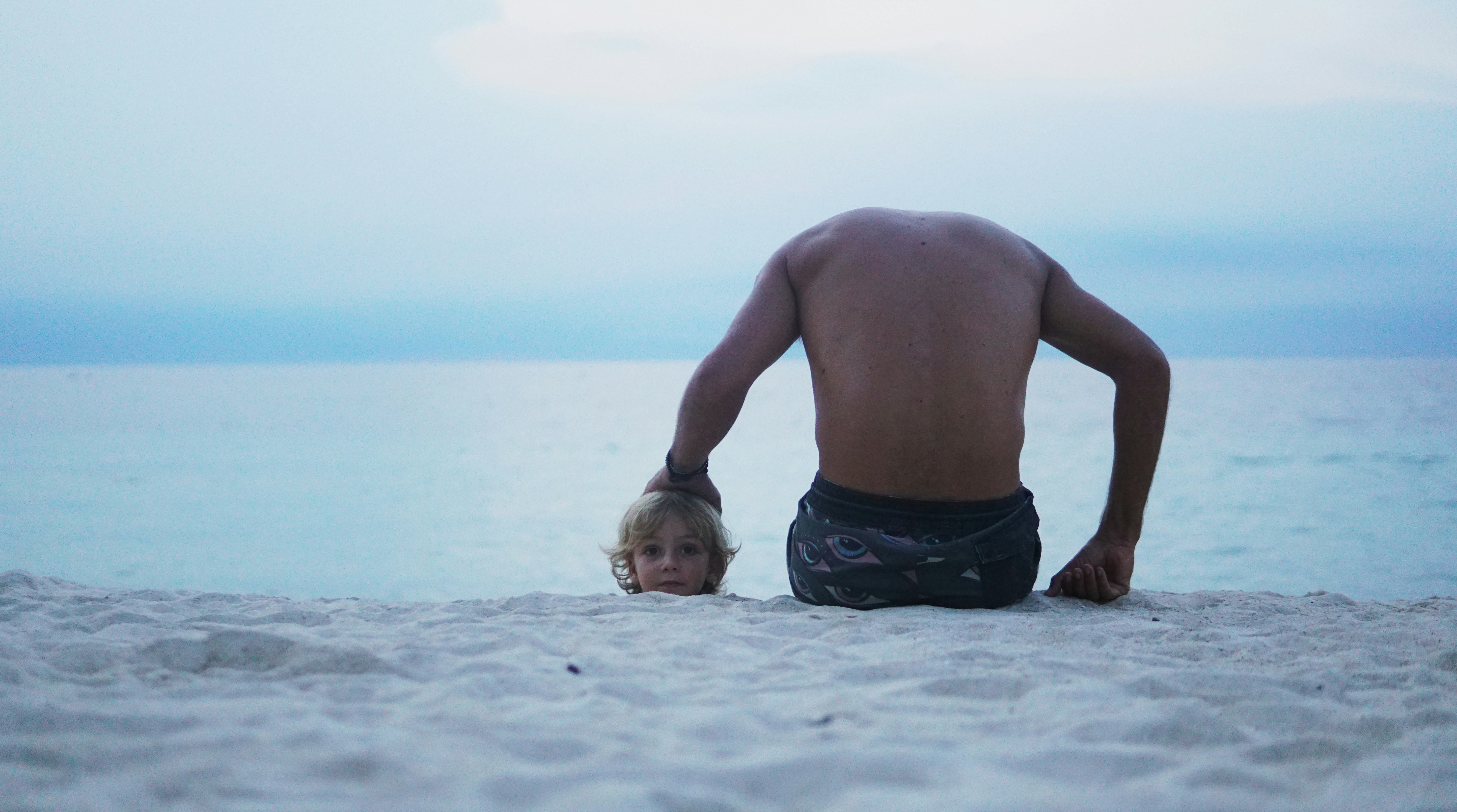 Emergence by the Tide: A Child Peeks from the Sand Beside a Beach Silhouette
