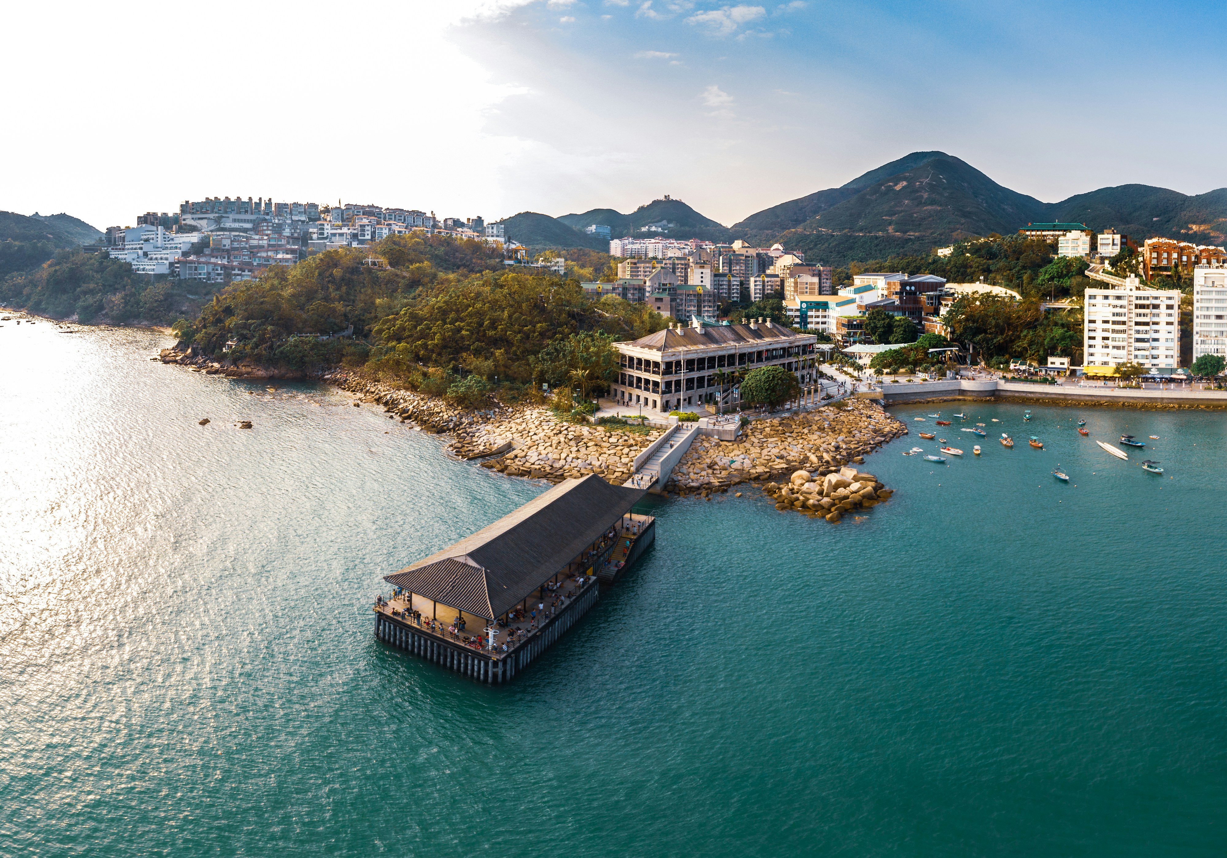 Aerial view of a coastal town with white buildings, lush hills, and clear blue waters.