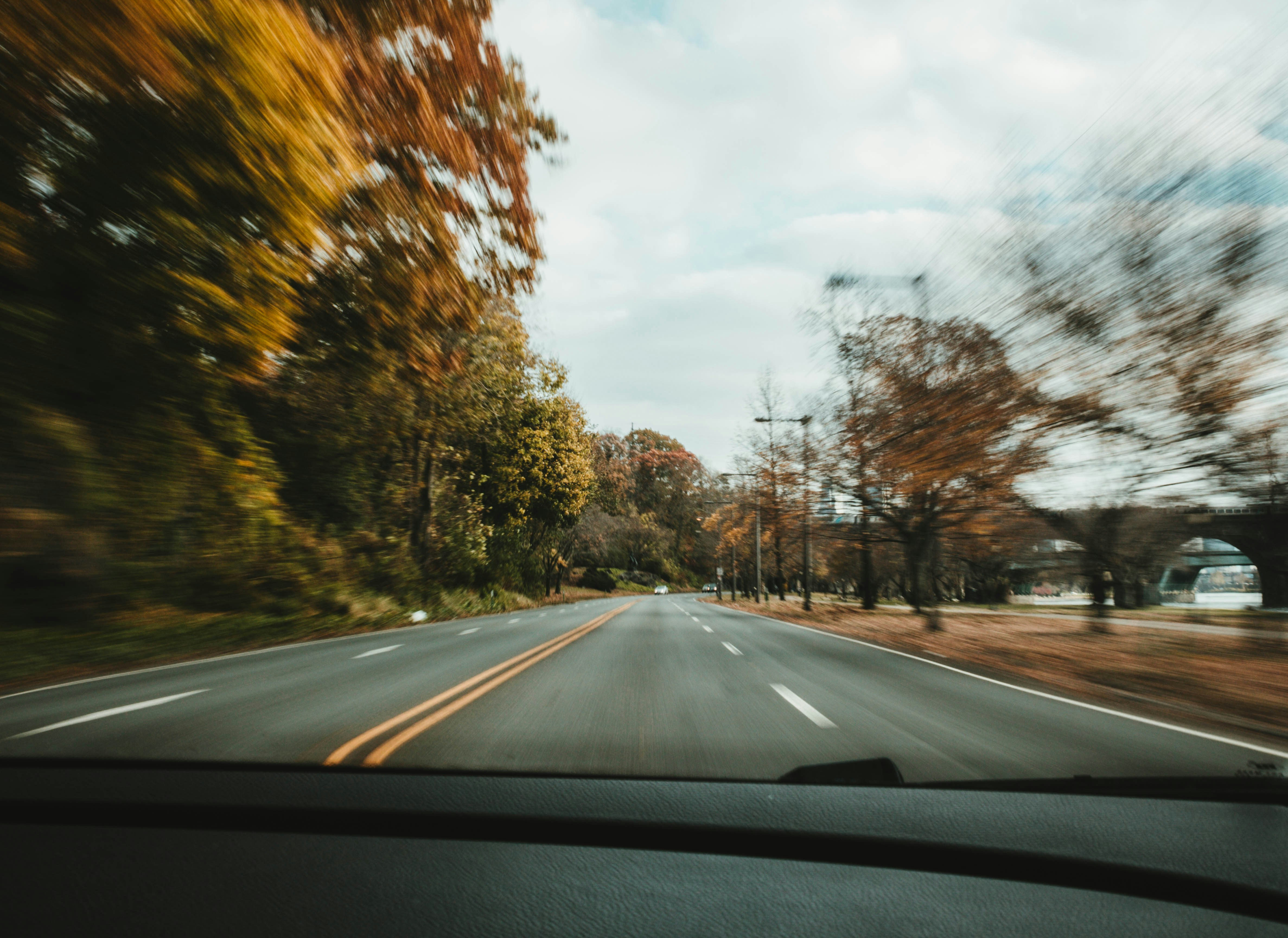 Blurred autumn trees line a road viewed from a moving car.