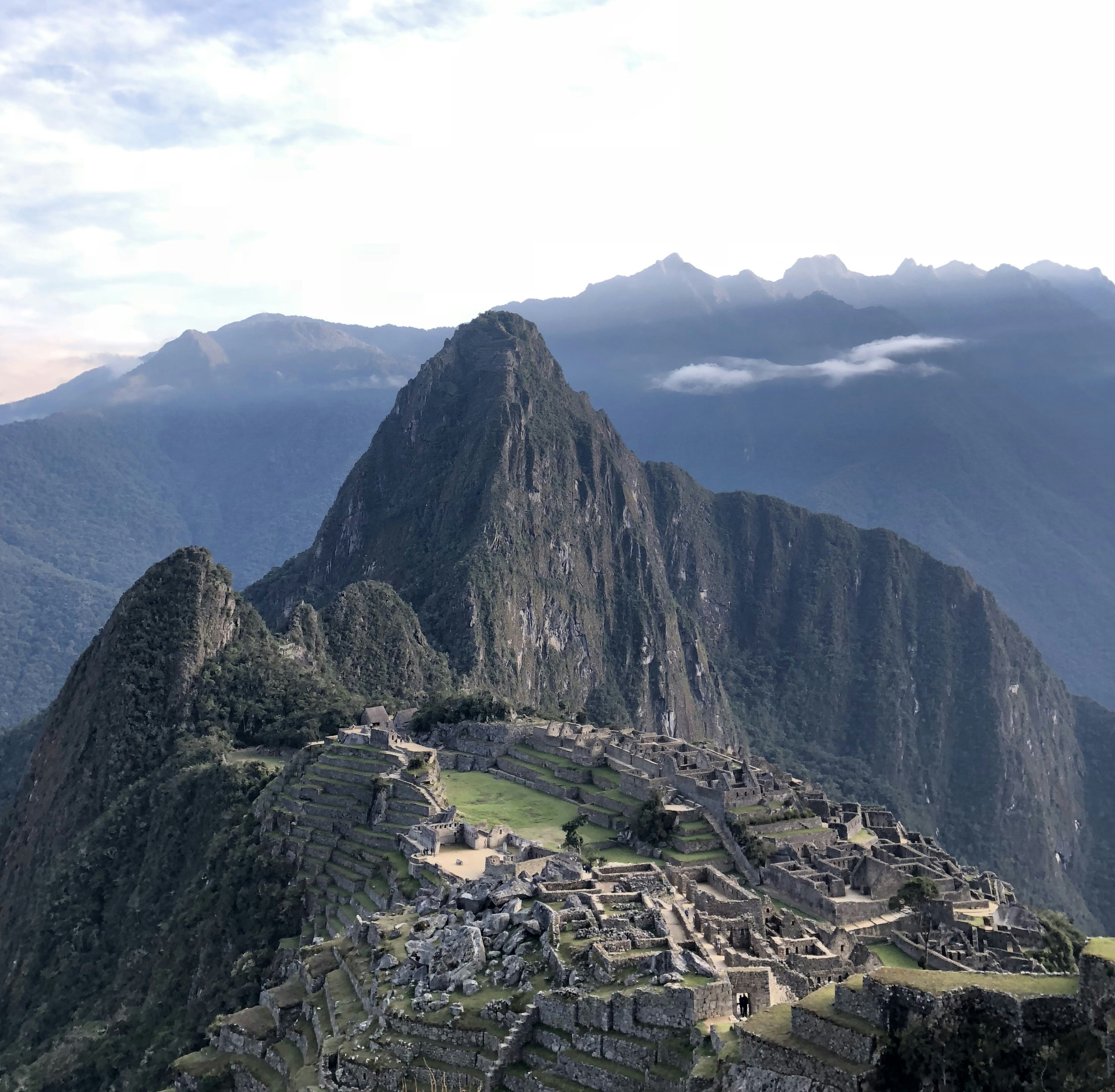 Machu Picchu's intricate stone structures nestled among lush green mountains under a cloudy sky.