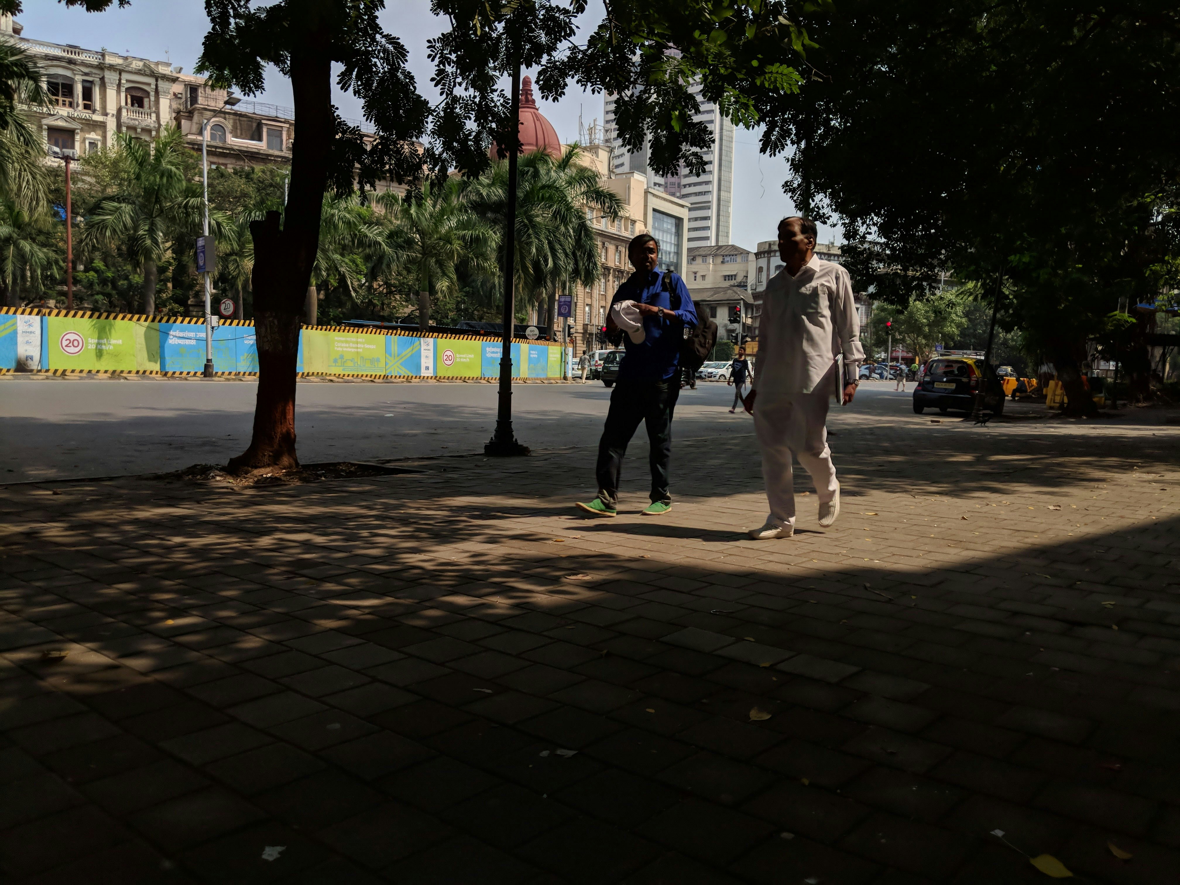 Two people walking on a tree-lined sidewalk with city buildings in the background.