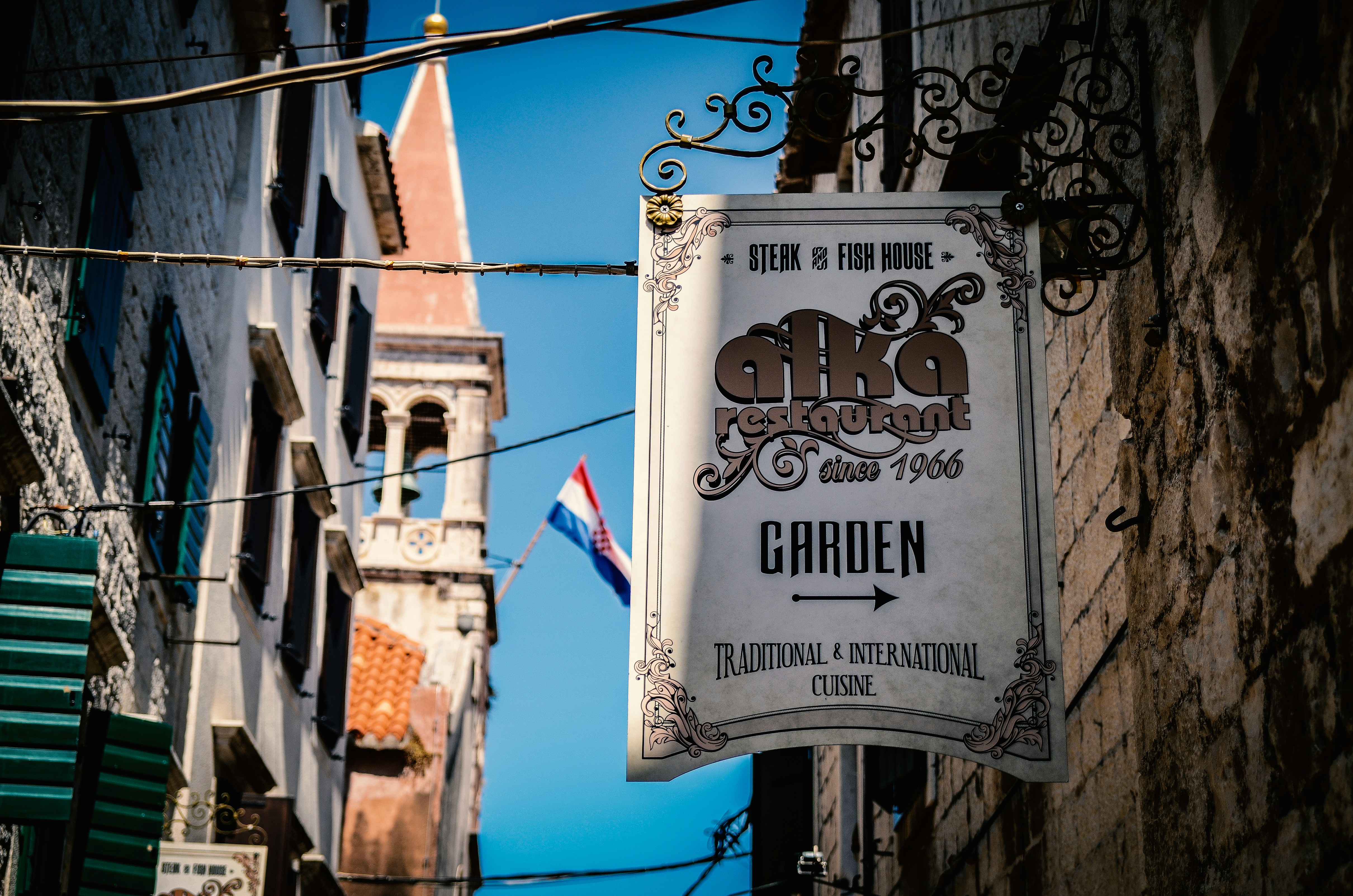 Garden Sign in a Sunlit Alley: Ornate Craft Meets Old Town Charm