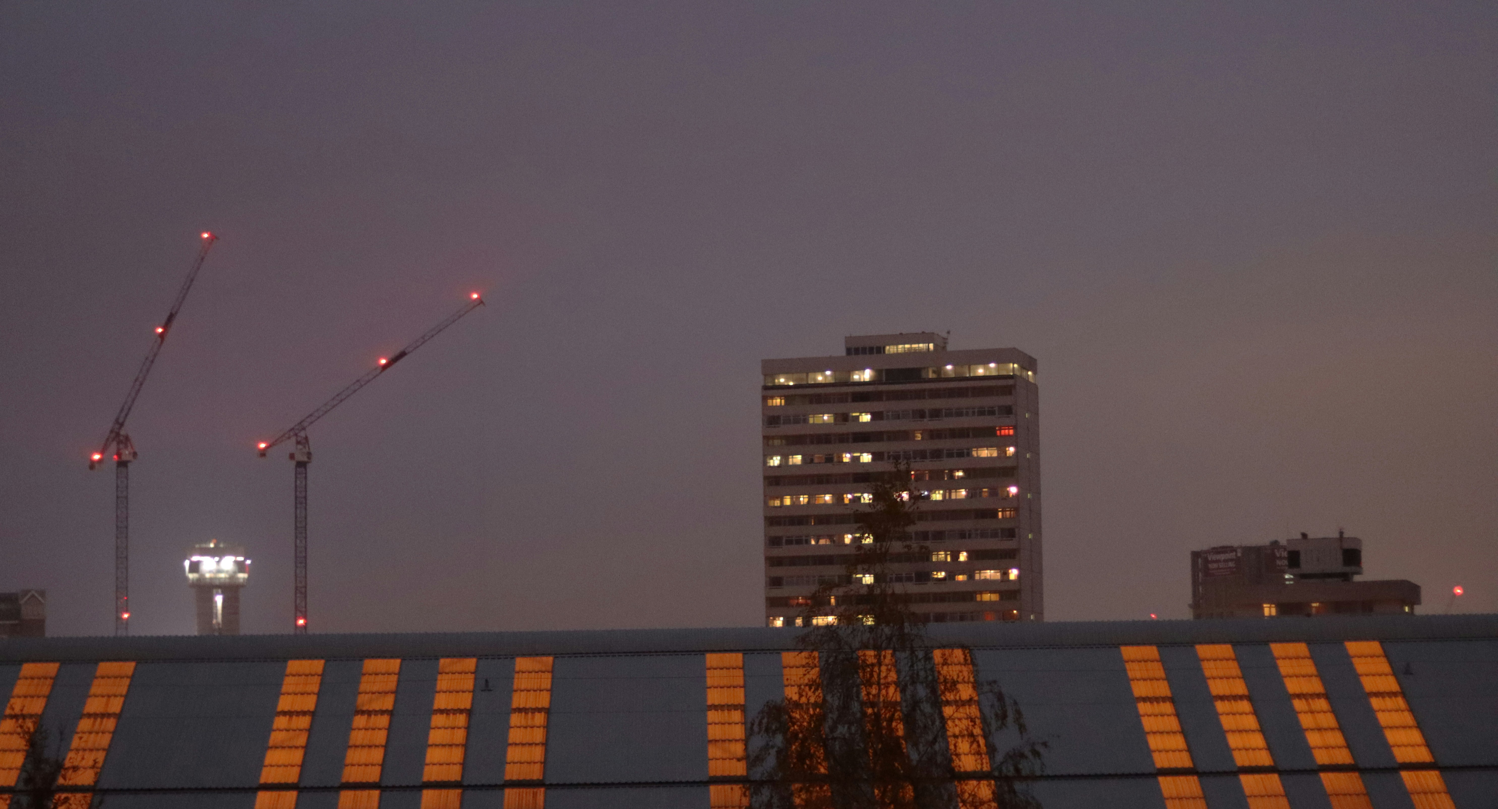 Nocturne Over the Rooftops: Cranes Framing a Luminous Tower
