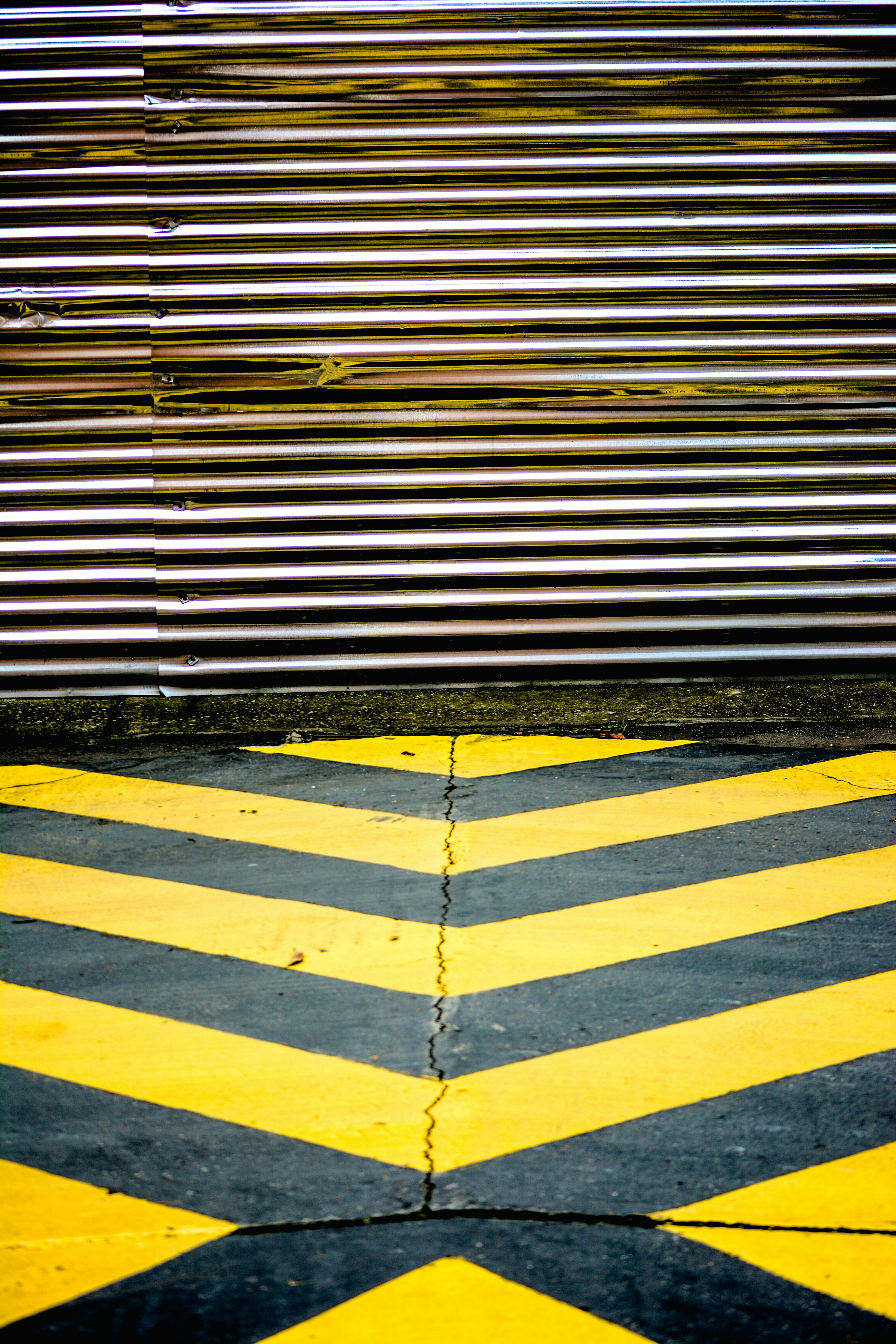 Industrial Crossing: Striped Convergence at the Base of a Metal Wall