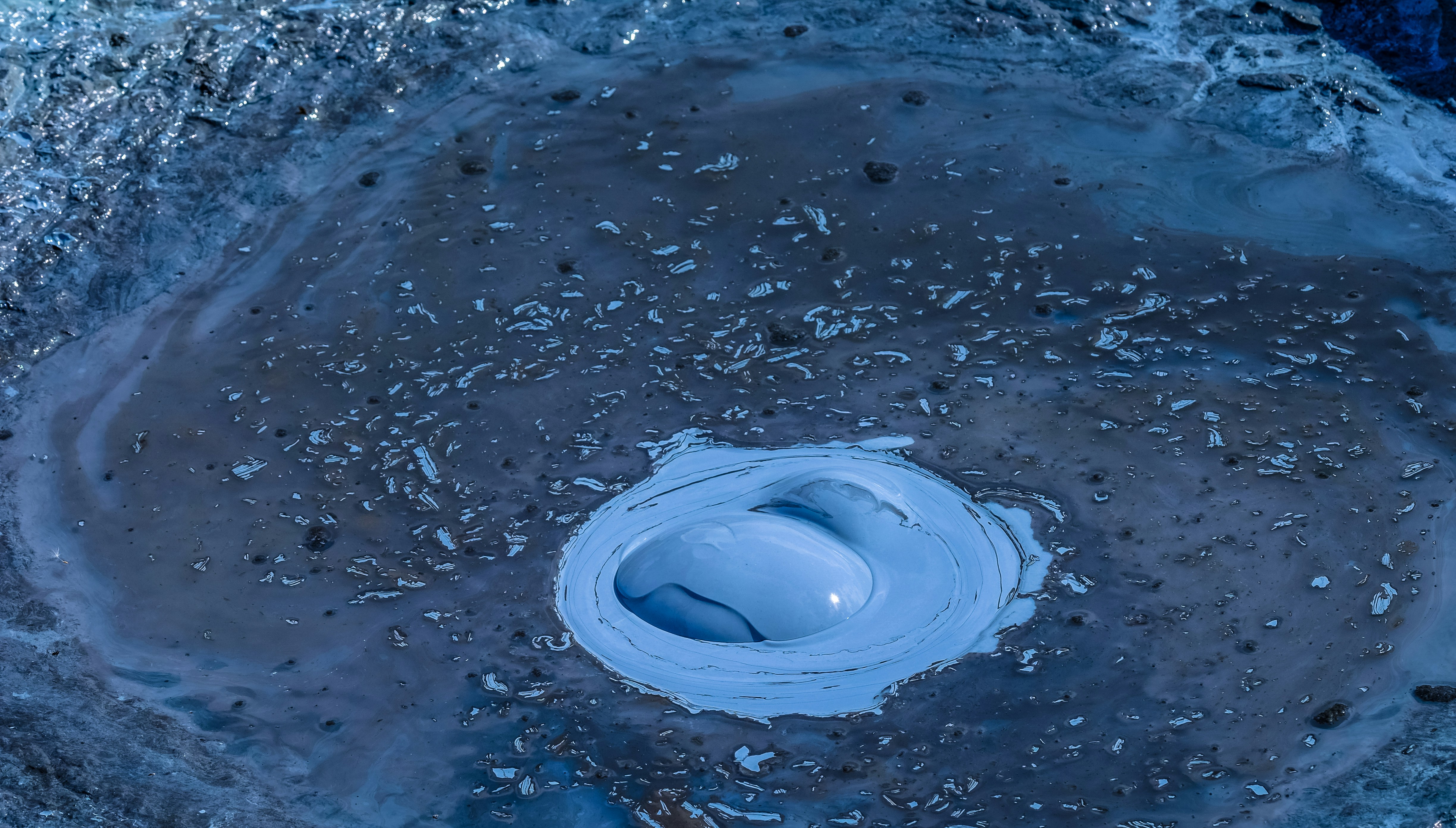 A mesmerizing blue bubble forms in a pool of liquid, surrounded by a textured surface that reflects light. The scene captures the unique interaction of color and form.