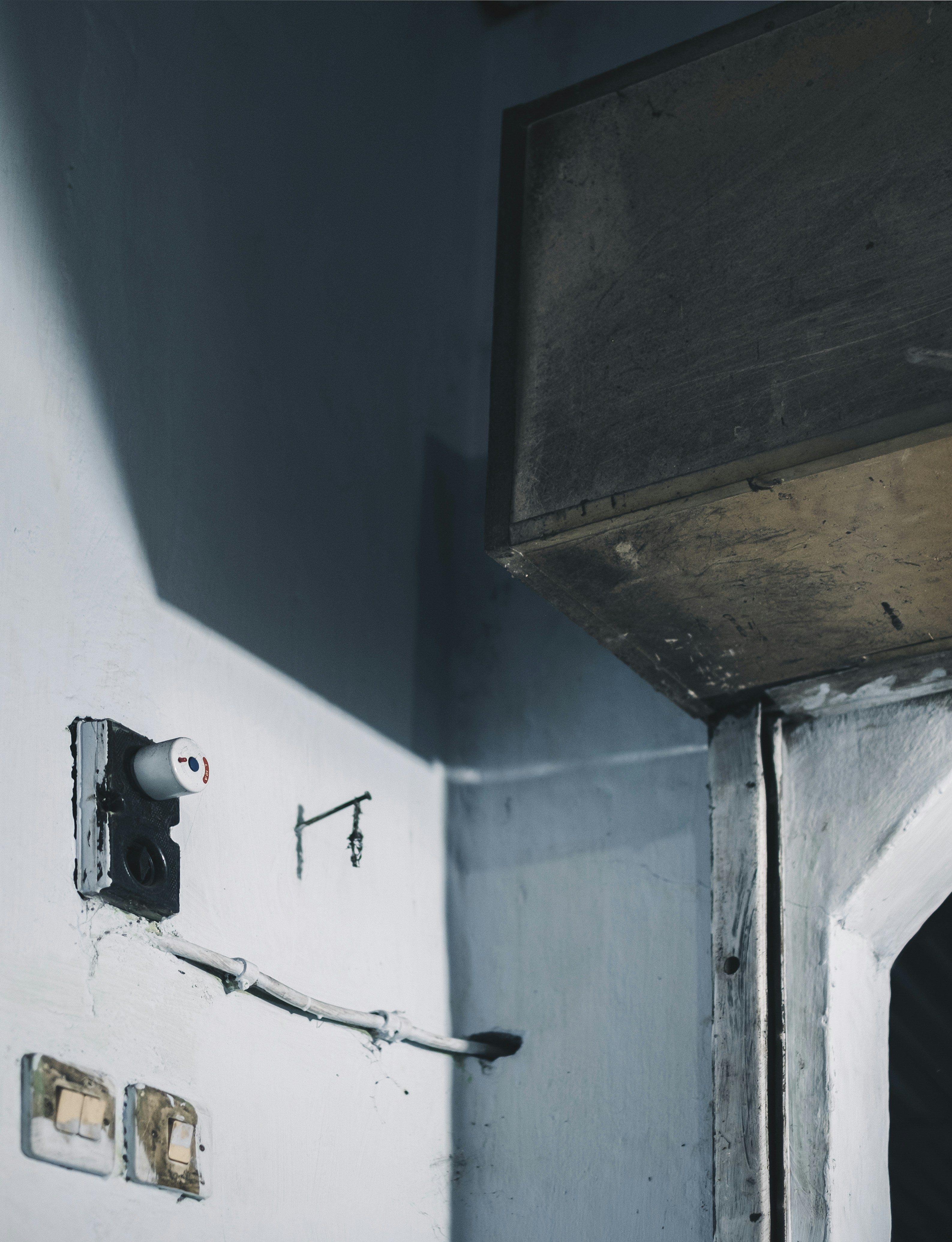 An old wall featuring a light switch, a hanging hook, and a mysterious object, illuminated by soft light. The scene captures a sense of neglect and history.