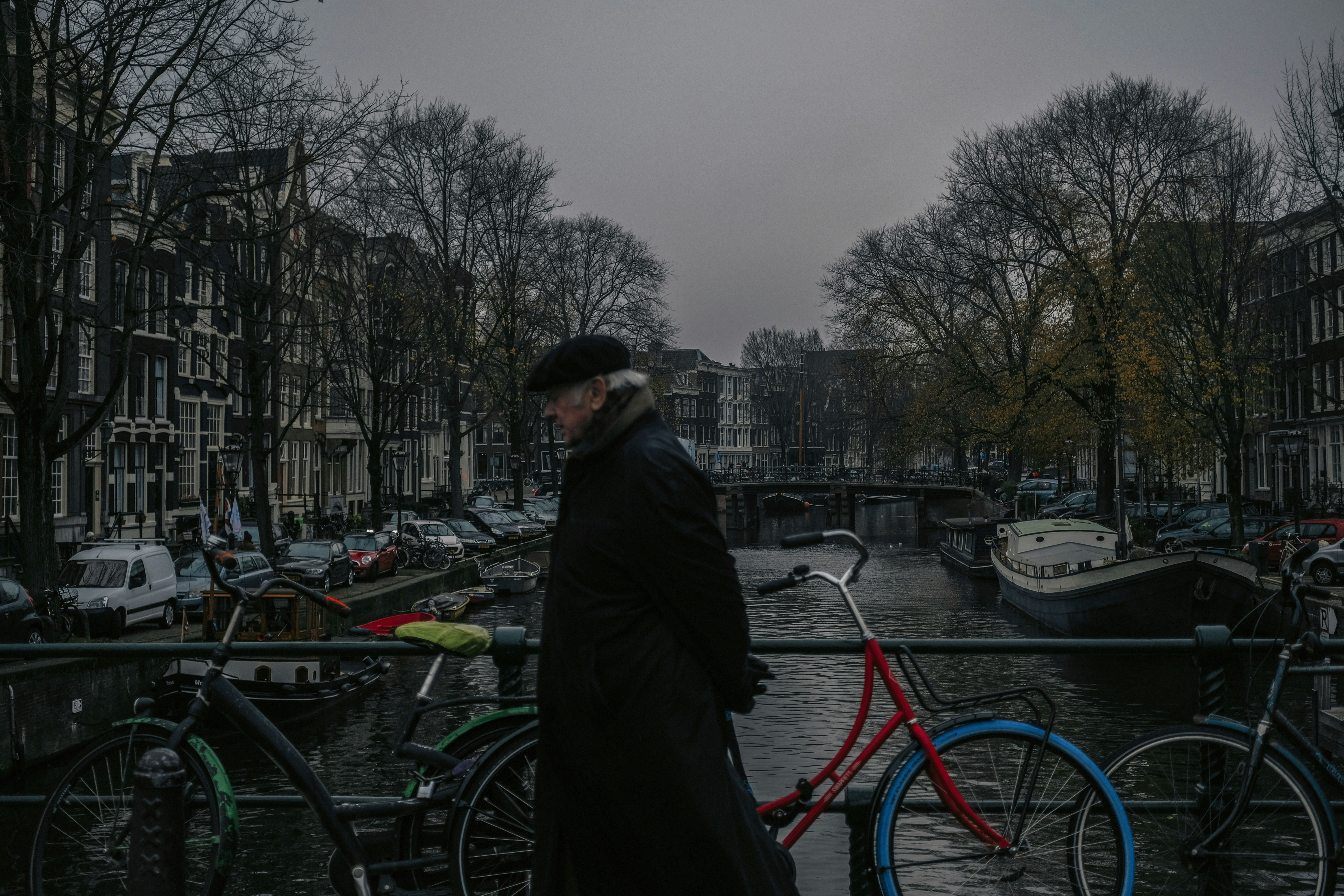 Crossing in the Grey: Pedestrian Amid Colorful Bicycles on a Wet Amsterdam Bridge