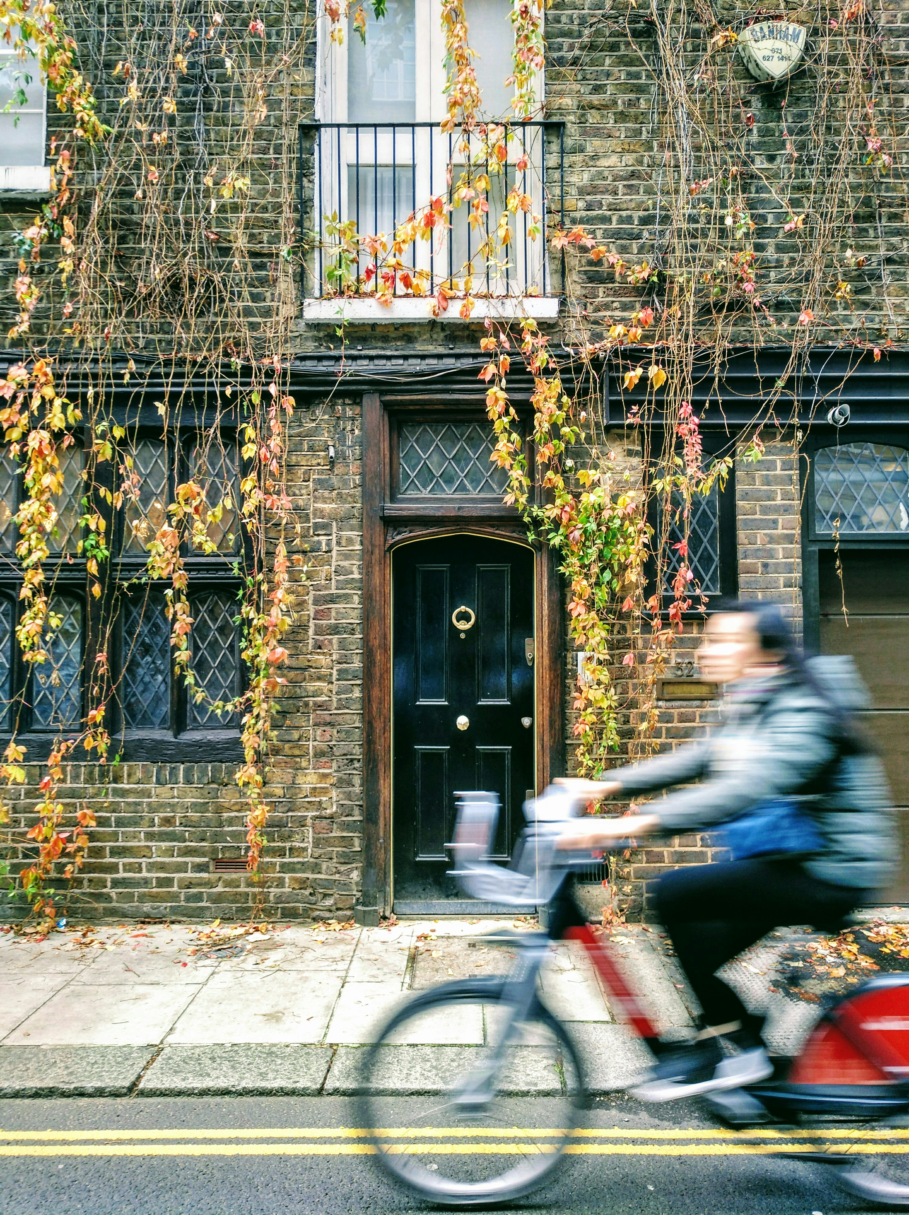Cyclist blurs past a brick building draped in autumn vines.