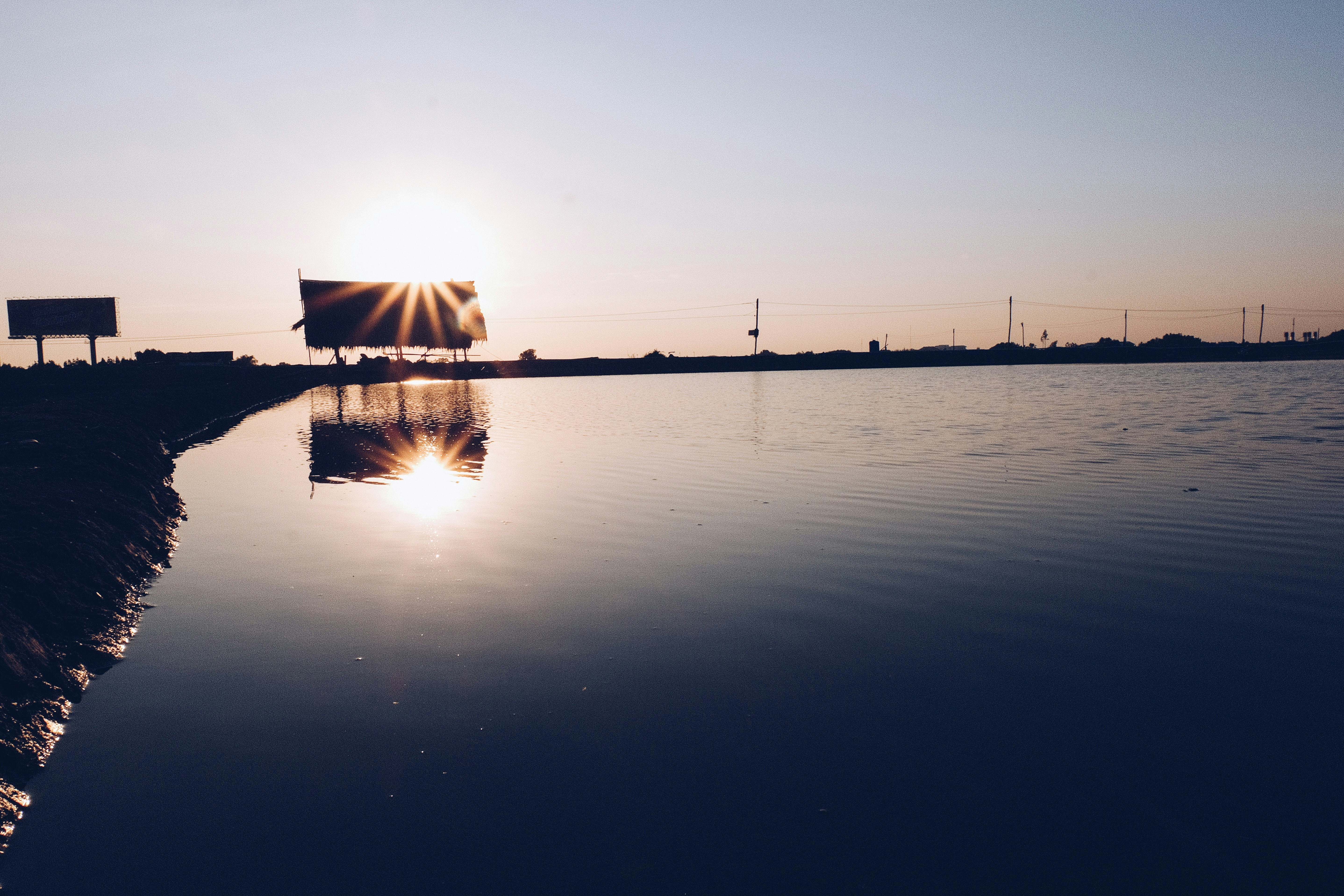 Sun setting behind a structure, casting reflections on a calm water surface.