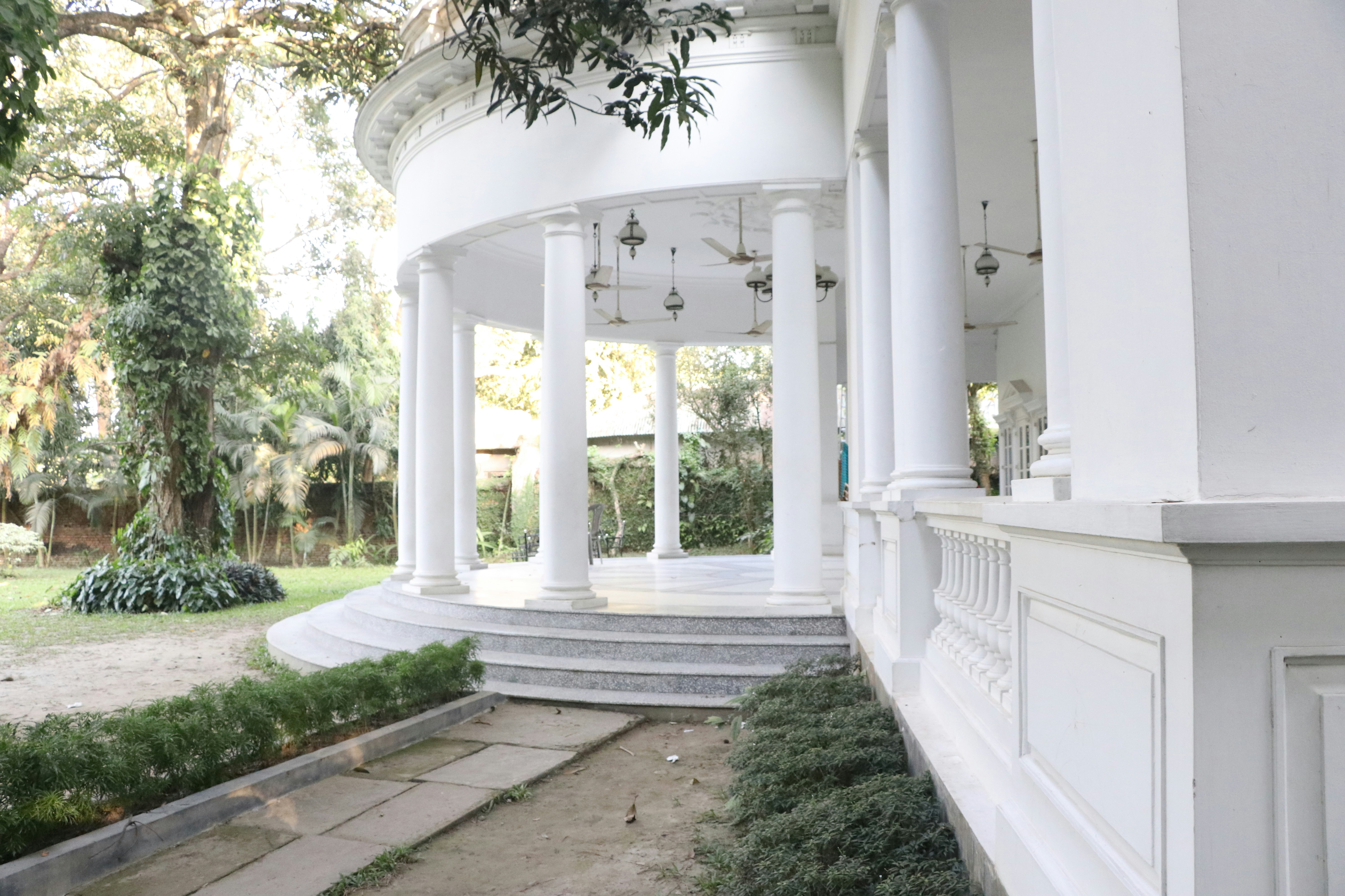 A beautifully designed colonial-style pavilion surrounded by lush greenery, showcasing intricate columns and tranquil pathways.