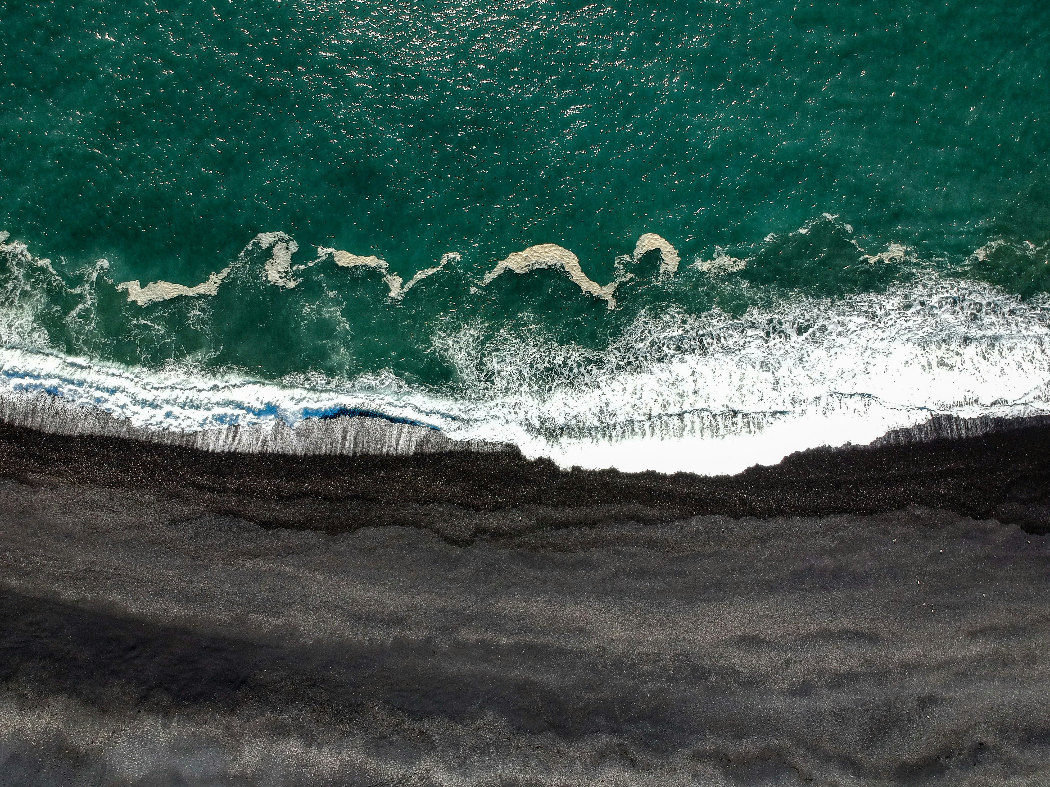 Aerial view of emerald ocean waves meeting a black sand beach with distinct contrast and texture.
