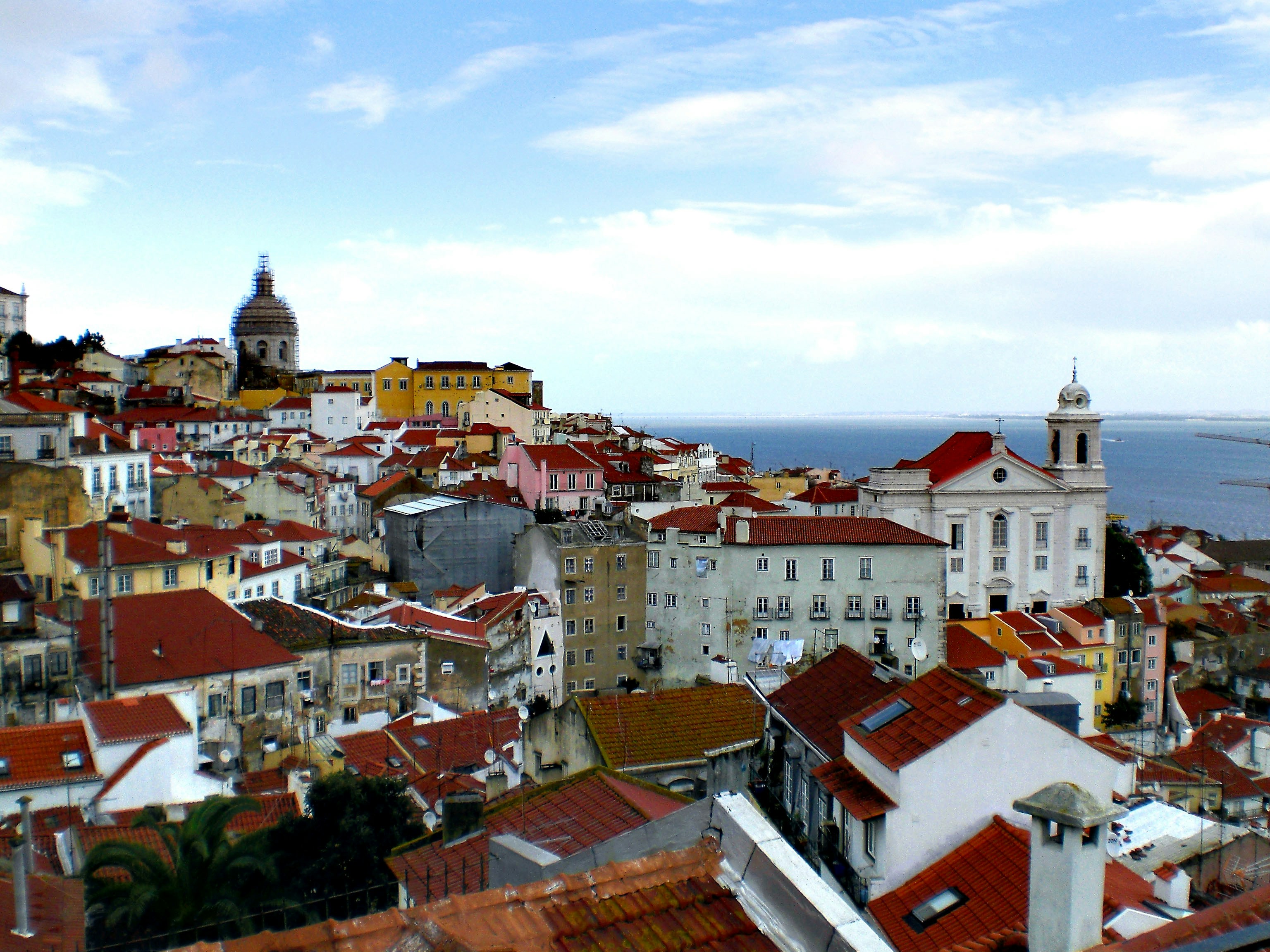 Vibrant rooftops of Lisbon's buildings, showcasing a mix of architectural styles and colors under a bright sky. The scene captures the essence of the city's charm and history.