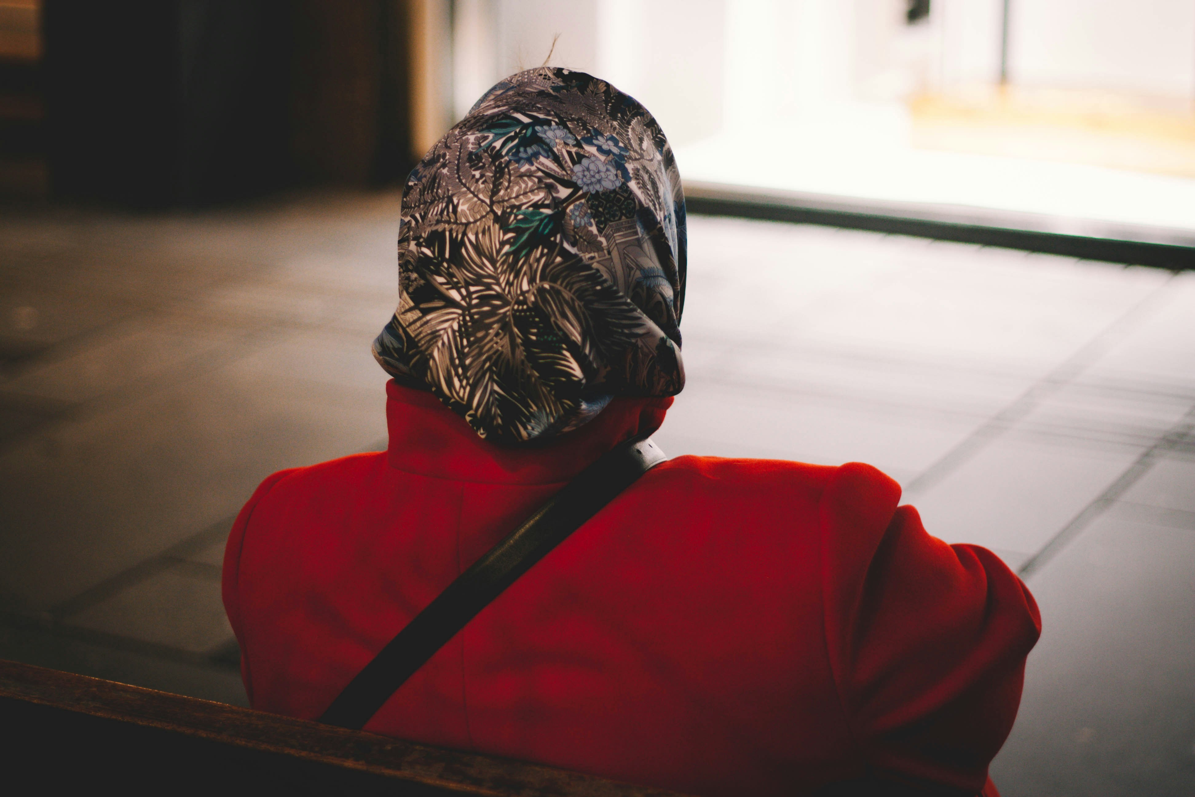 Person in a red coat sitting on a bench, facing a bright, open doorway.