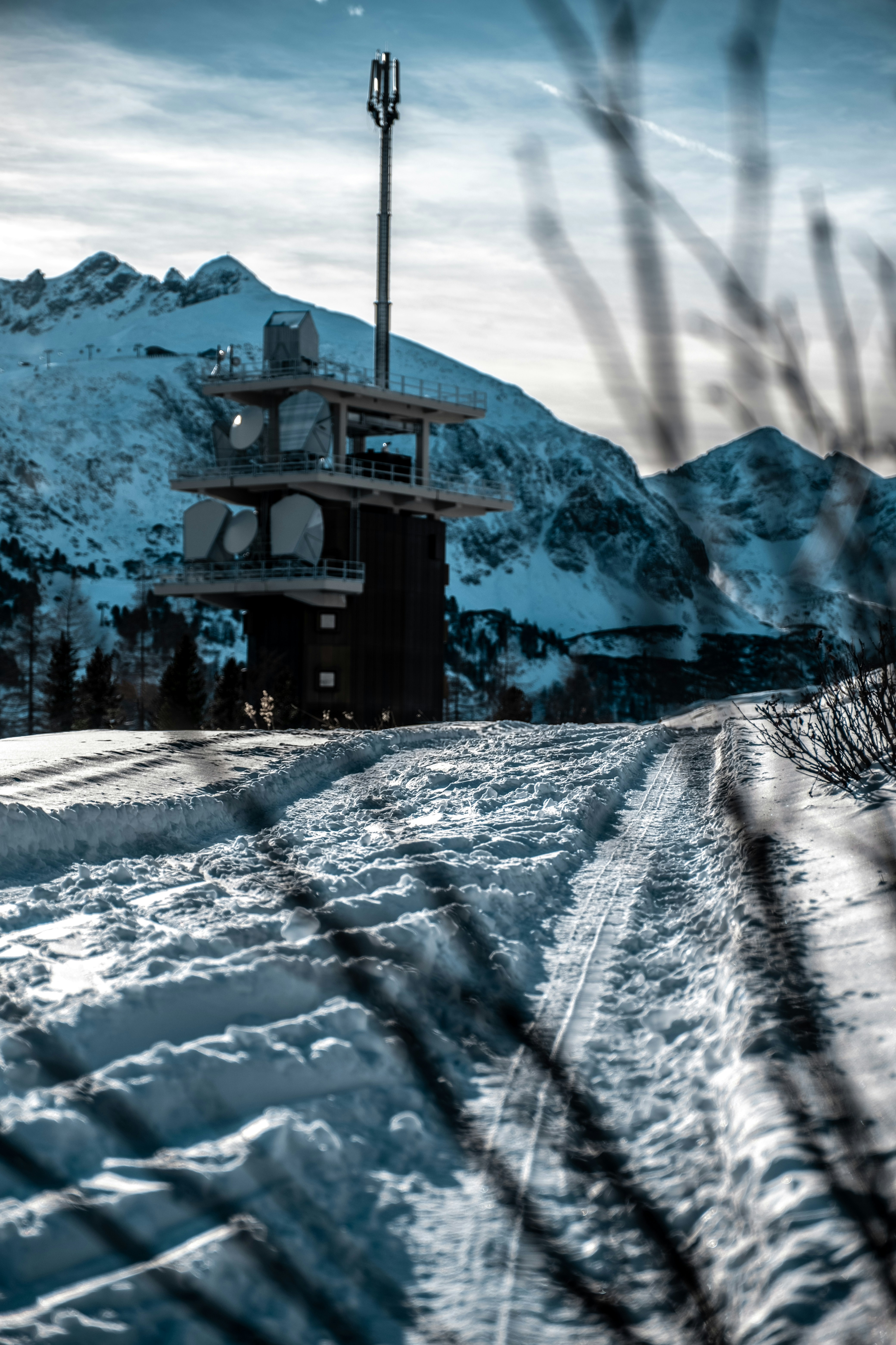 A telecommunications tower stands amidst a snowy landscape, framed by distant mountains under a clear sky.