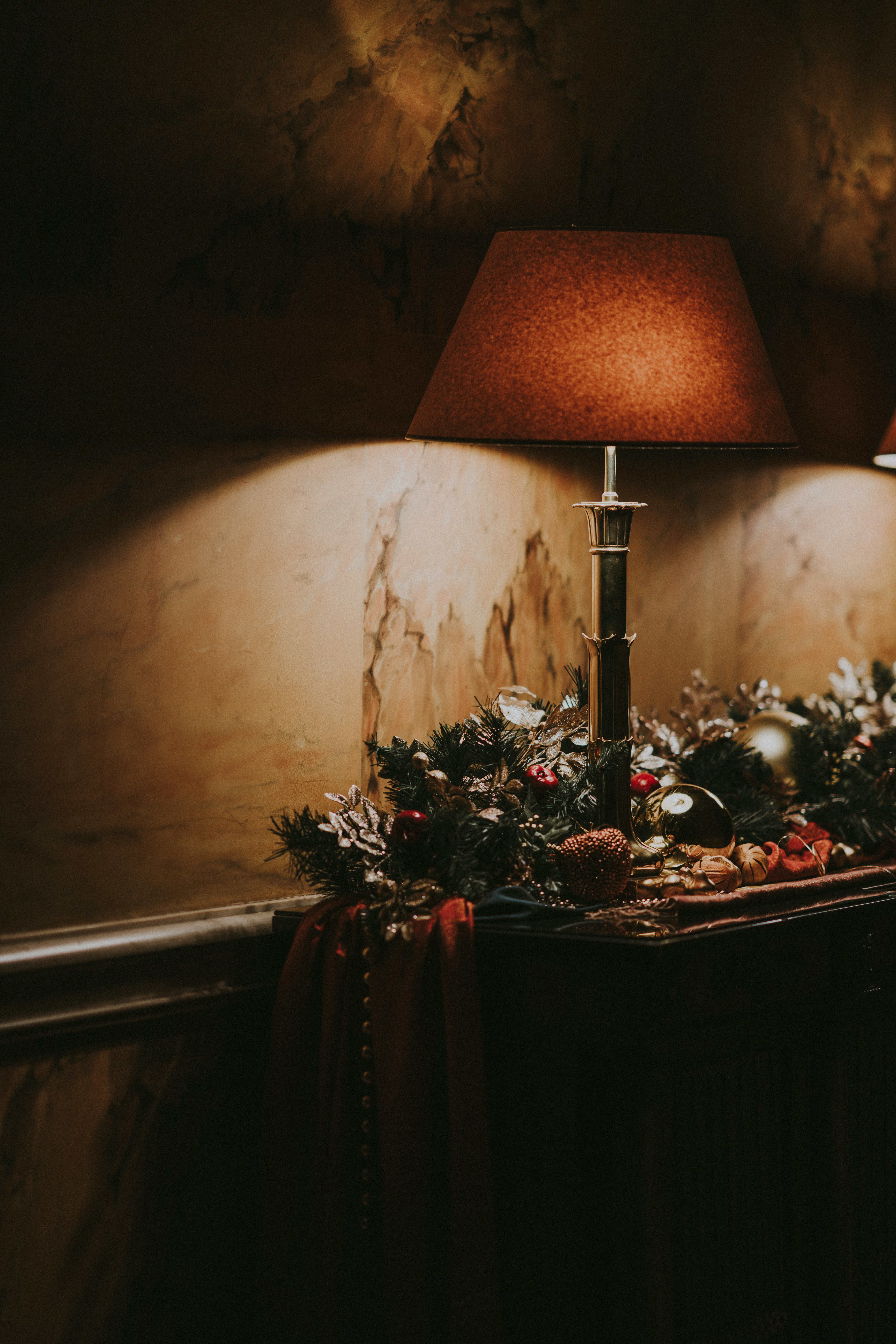 A beautifully arranged holiday centerpiece featuring a lamp and festive decorations on a table, radiating warmth in a dimly lit room.