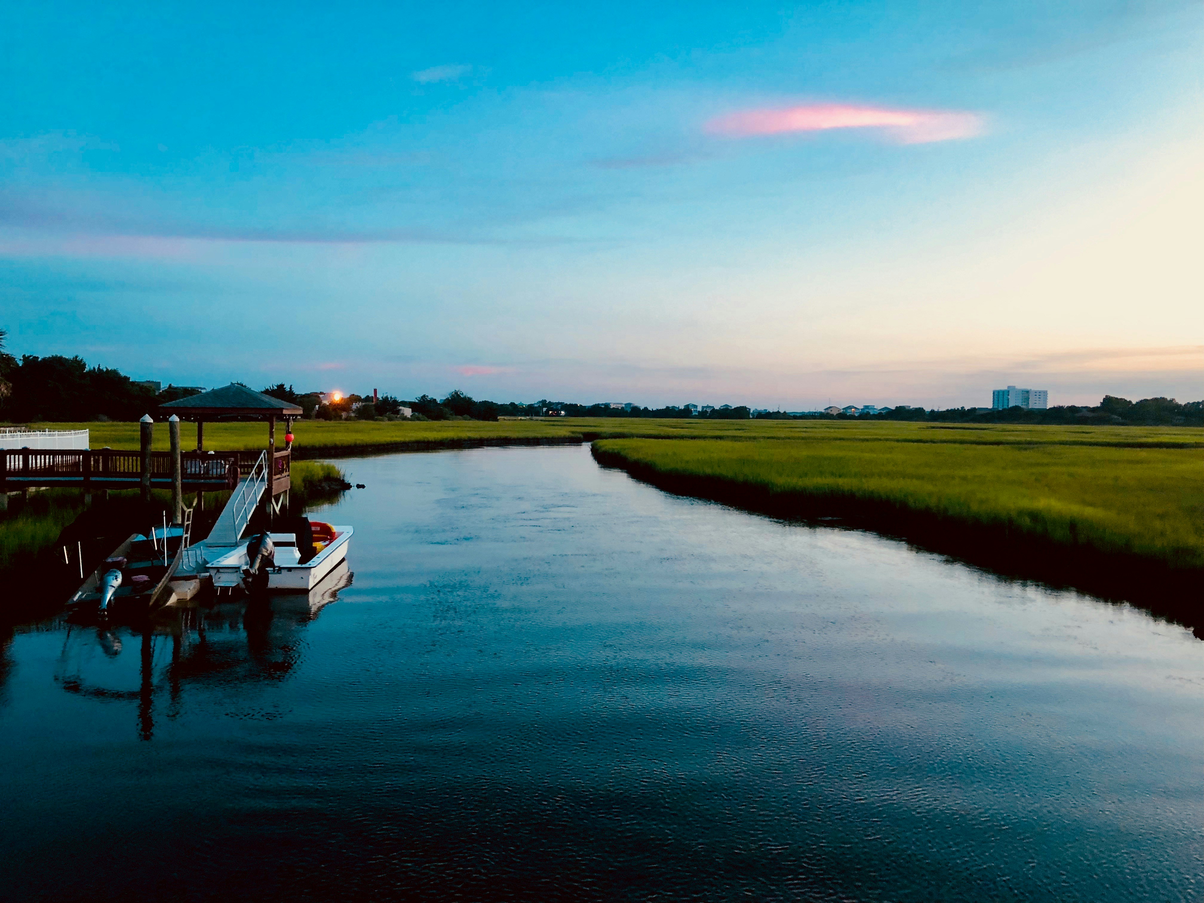 Calm waterway reflecting the pastel hues of a sunset sky, bordered by lush green marshland.