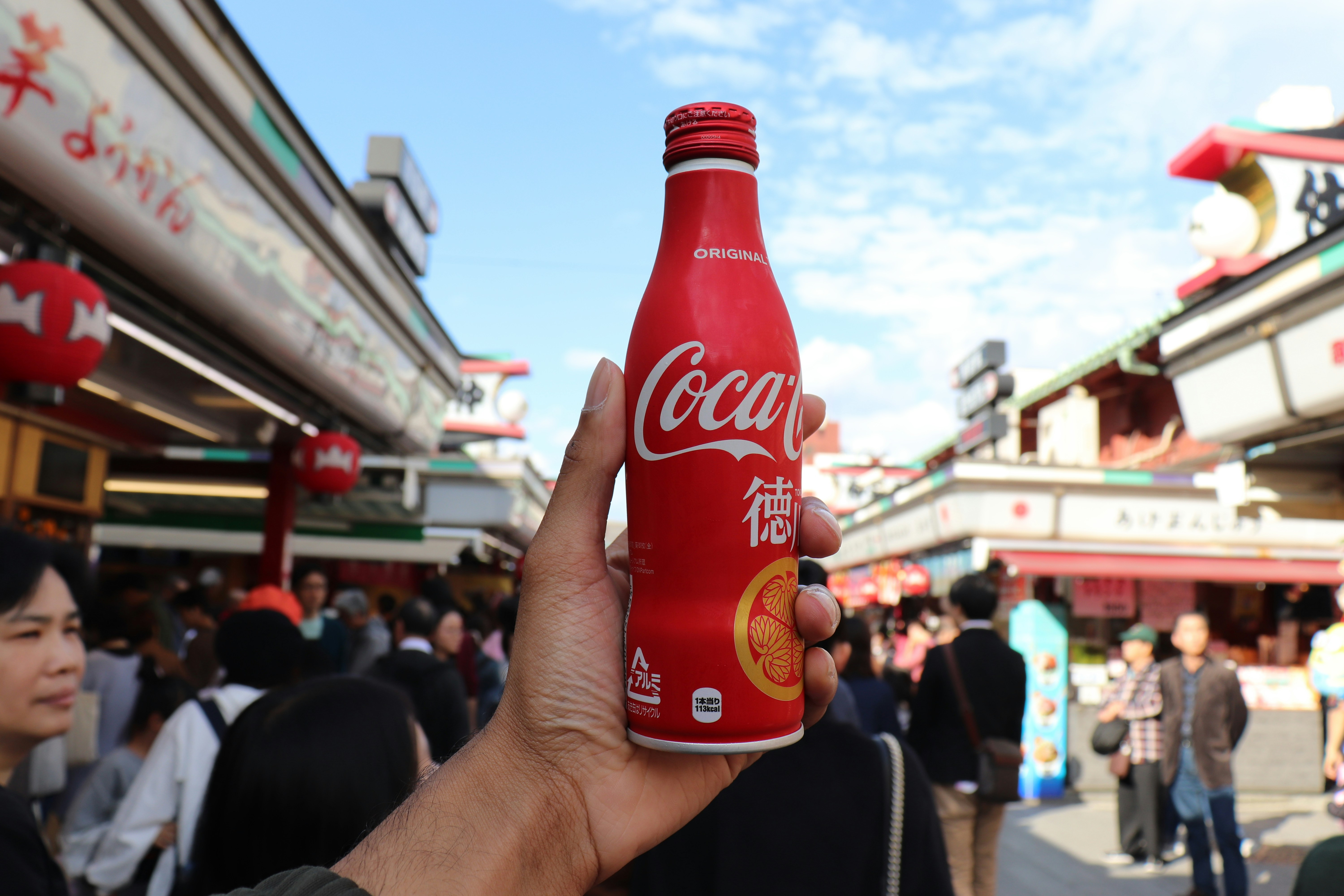 Persona sosteniendo una botella roja de Coca Cola cerca de la multitud ...