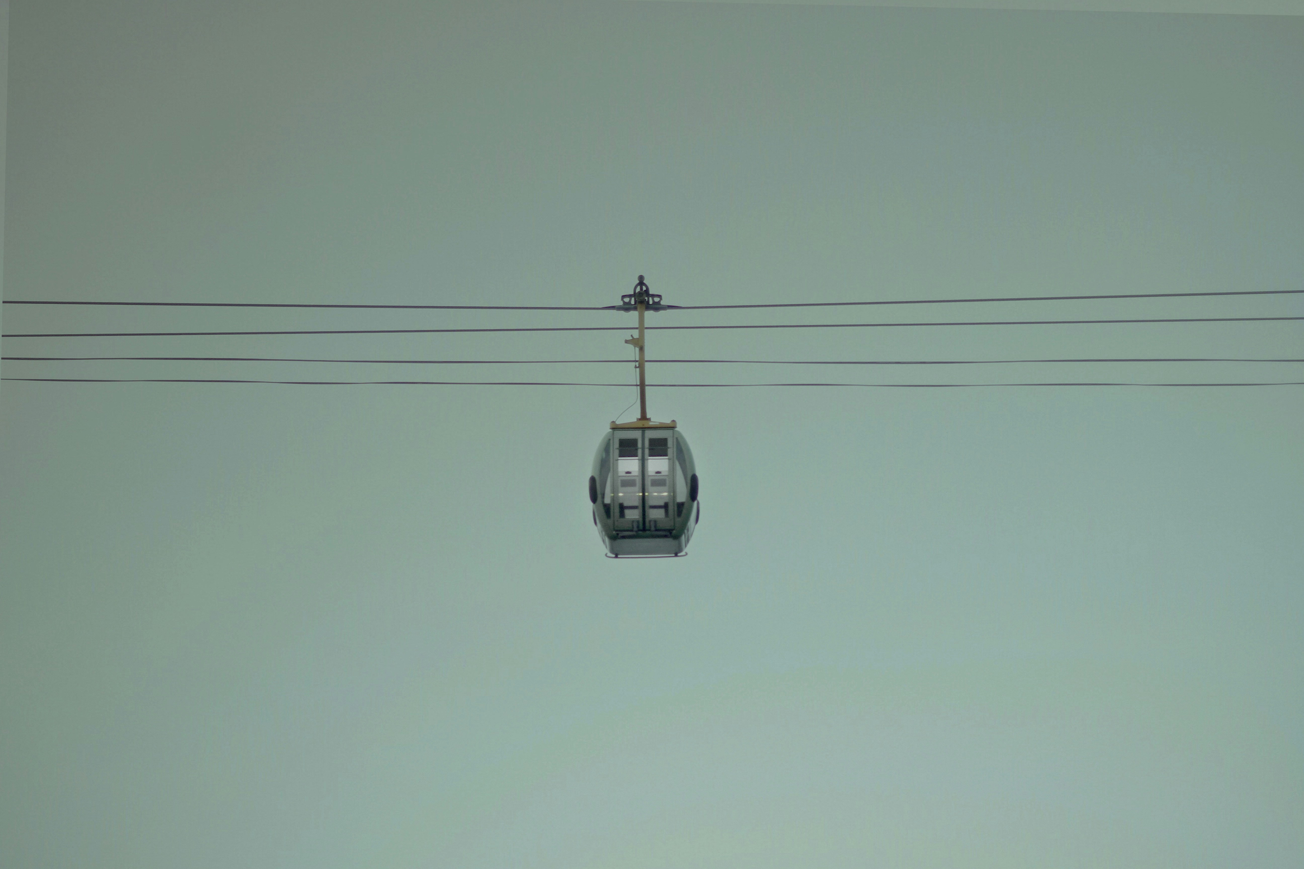 Pastel Ascent: A Lone Gondola Crossing a Minimal Sky