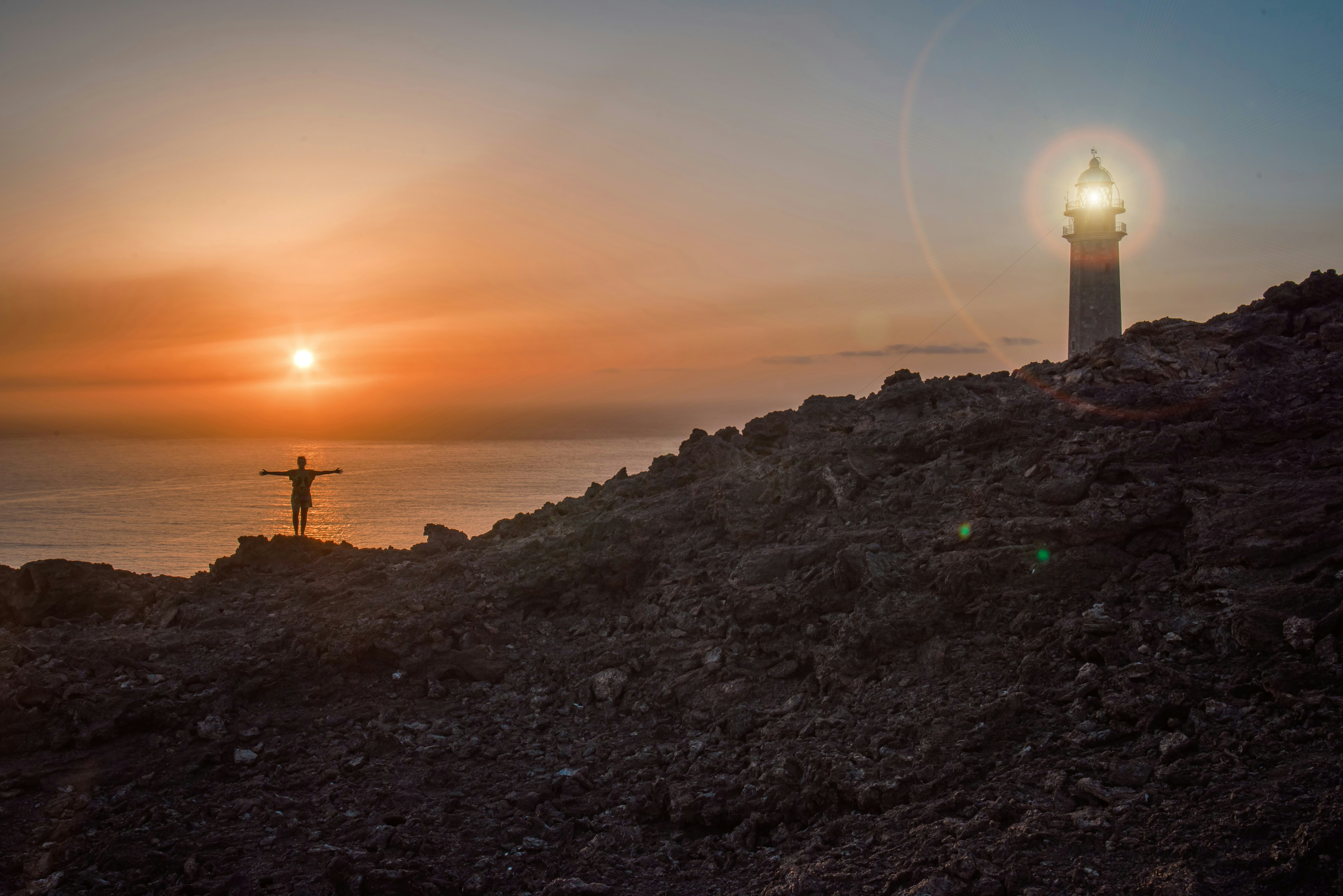 Man standing with arms wide open near lighthouse during golden hour ...