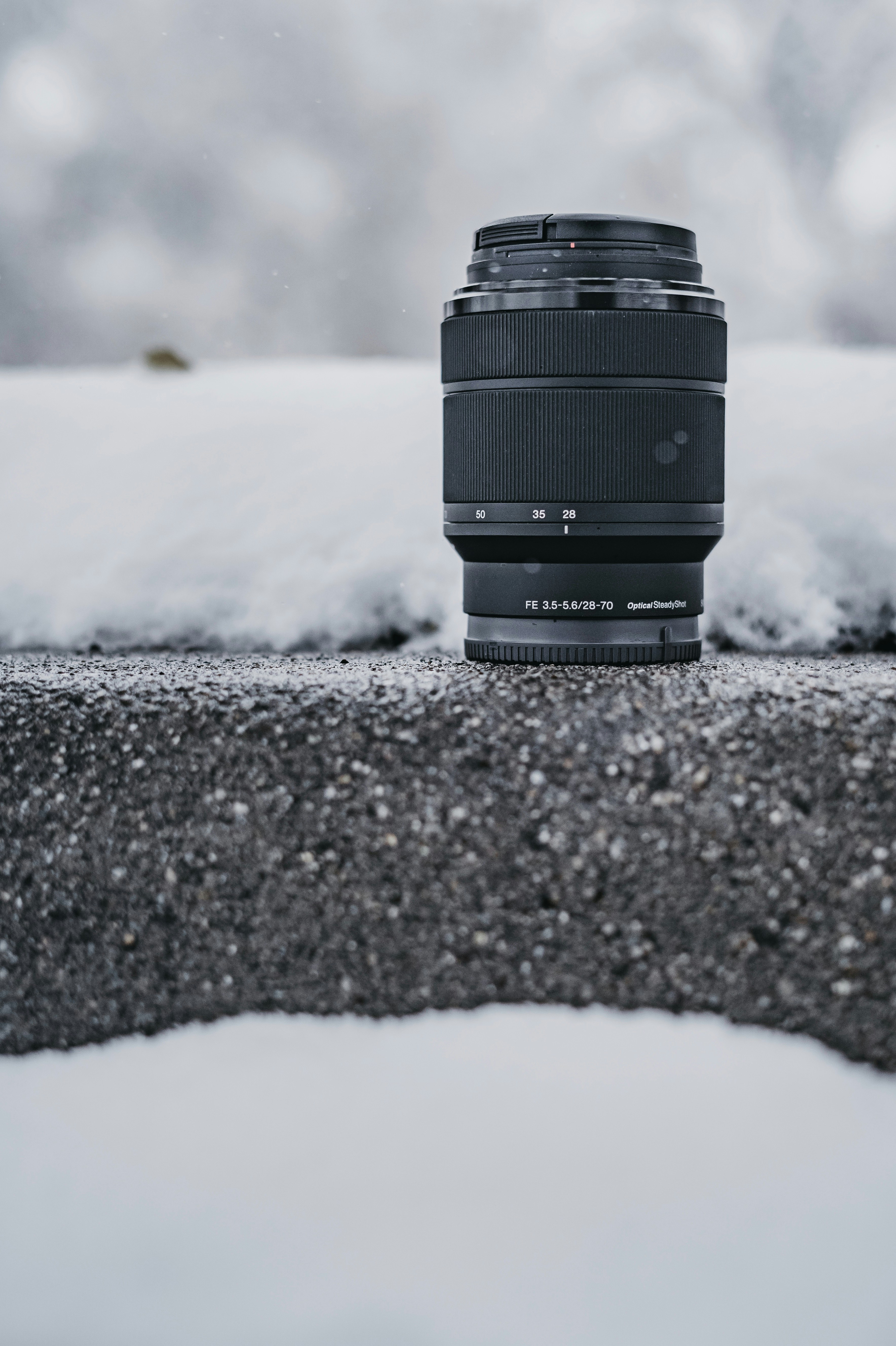 Camera lens resting on a textured surface, surrounded by a blanket of snow. The scene captures the essence of winter photography gear.