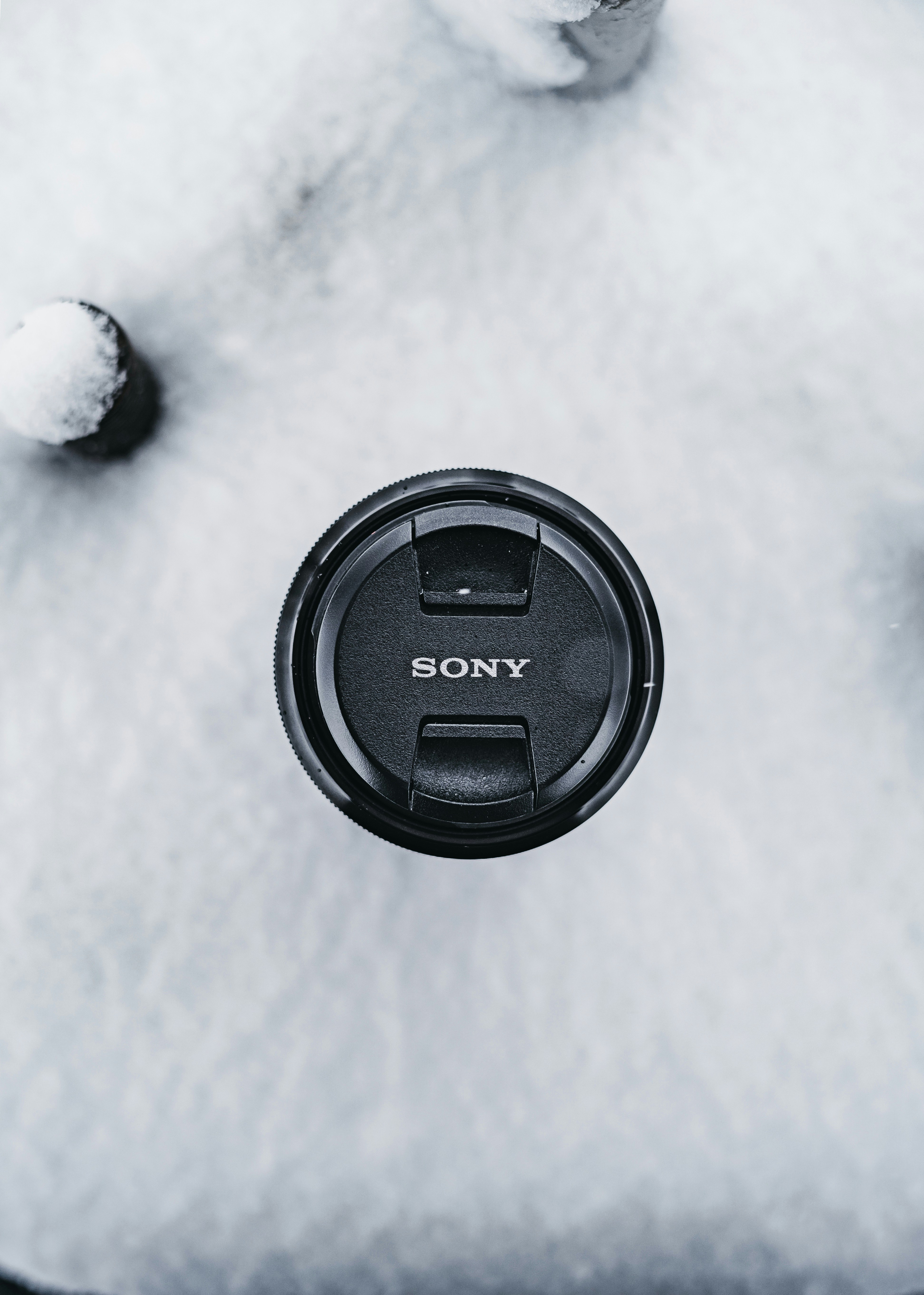Sony lens cap resting on a blanket of fresh snow, surrounded by soft, snow-covered elements.
