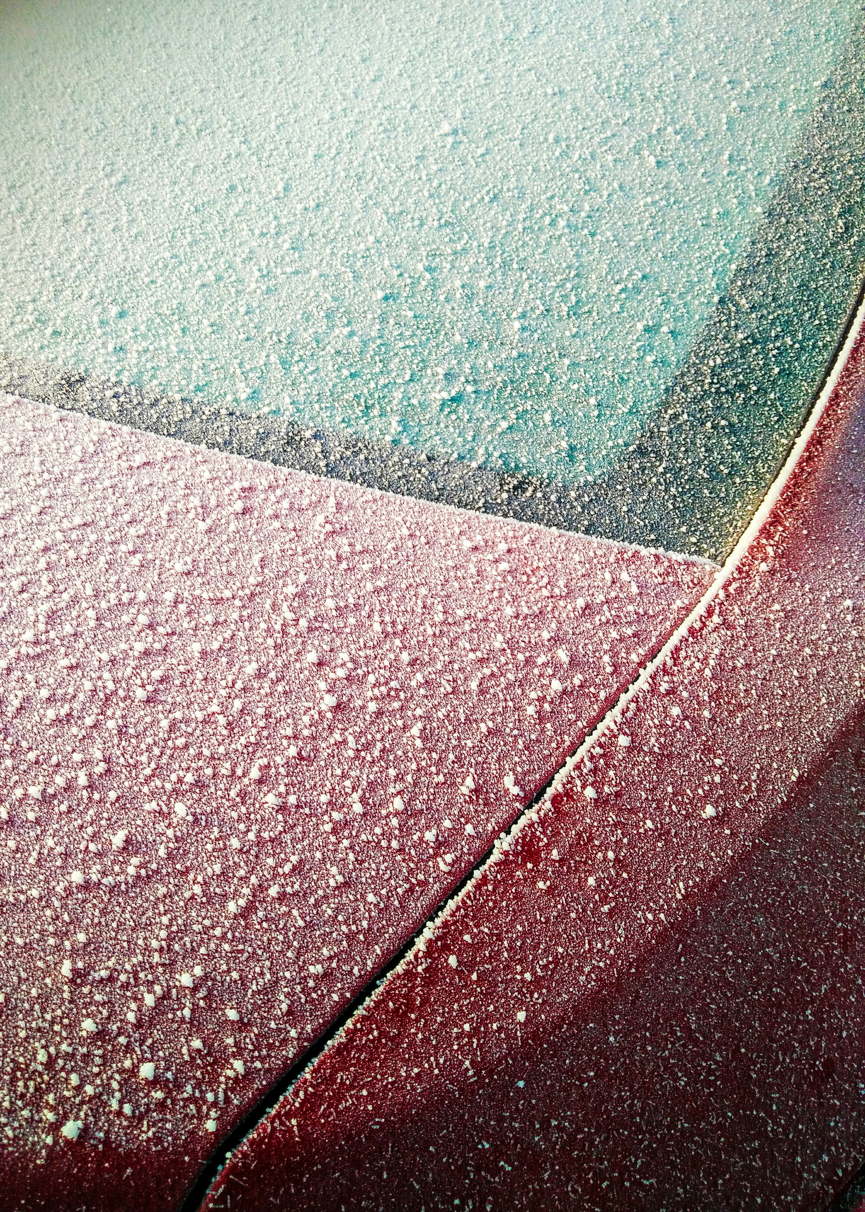 Close-up photograph of a frosted, two-tone car panel with a curved seam, featuring pastel teal and pink surfaces. The crystalline frost creates speckled texture across the paint.