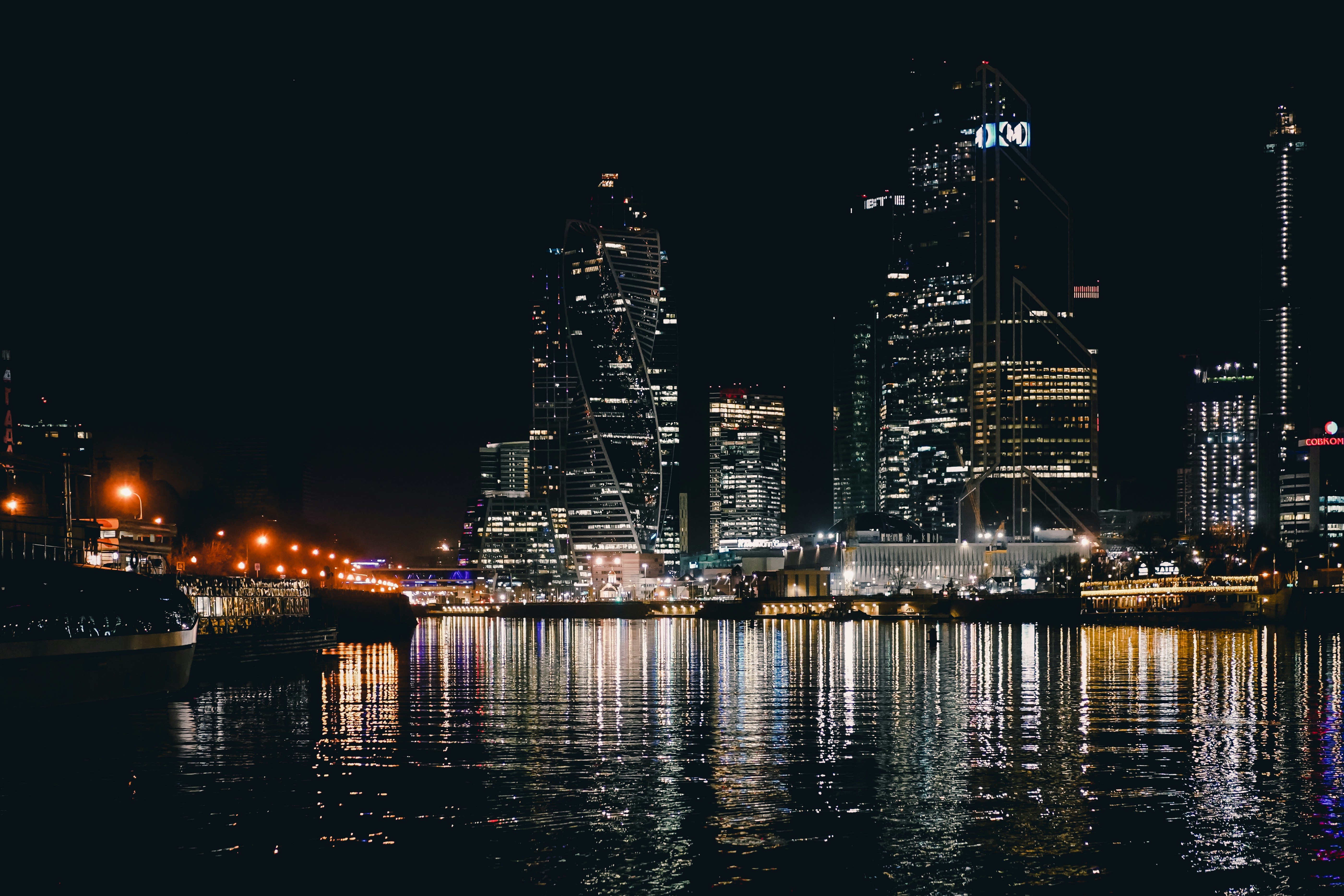 High-rise buildings illuminated against a night sky, reflected in a calm body of water.