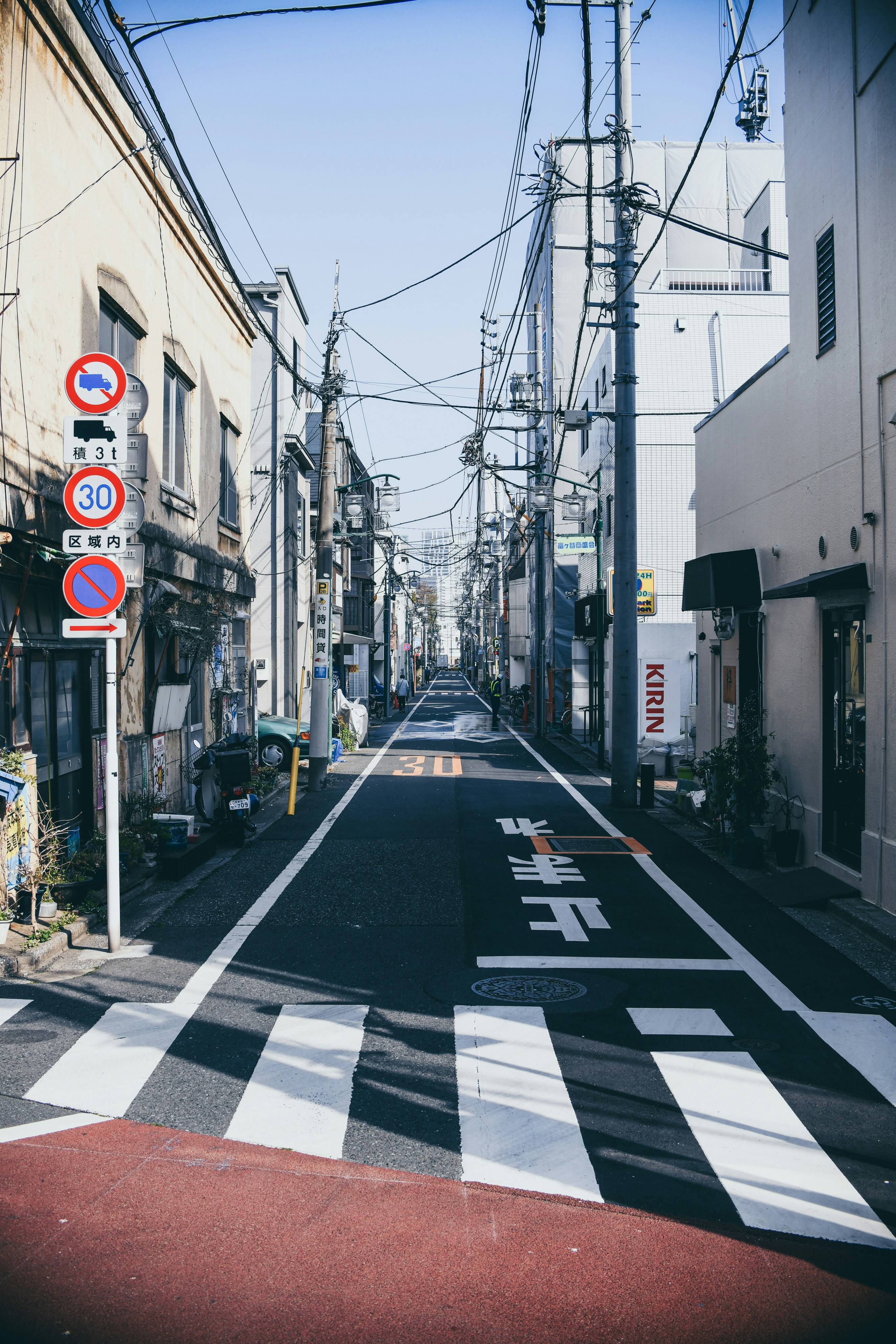 Narrow city street lined with utility poles and signage, showcasing the intricate web of overhead wires and the quiet charm of urban living.