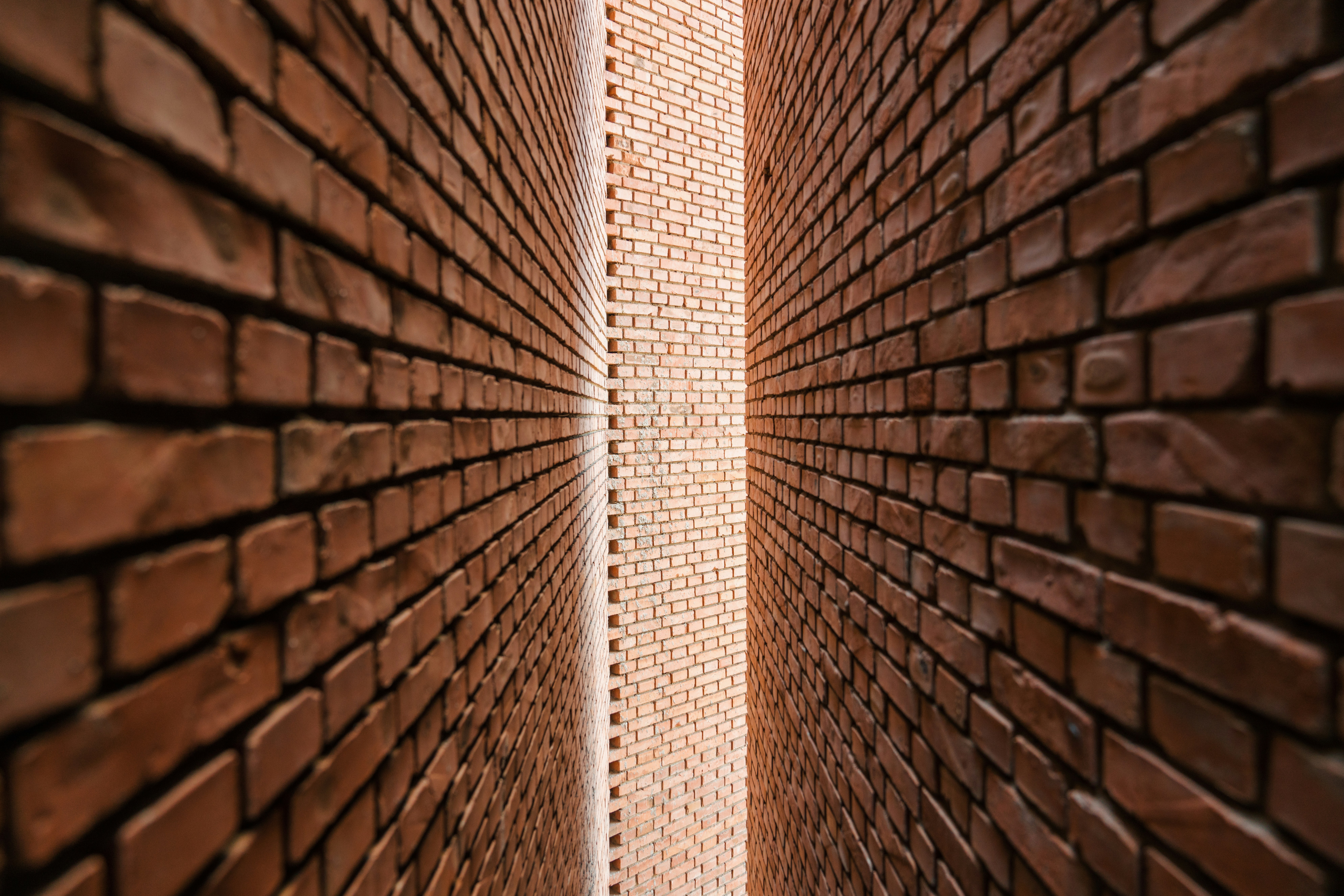 Narrow passage of brown brick walls converging towards a lit central corner.