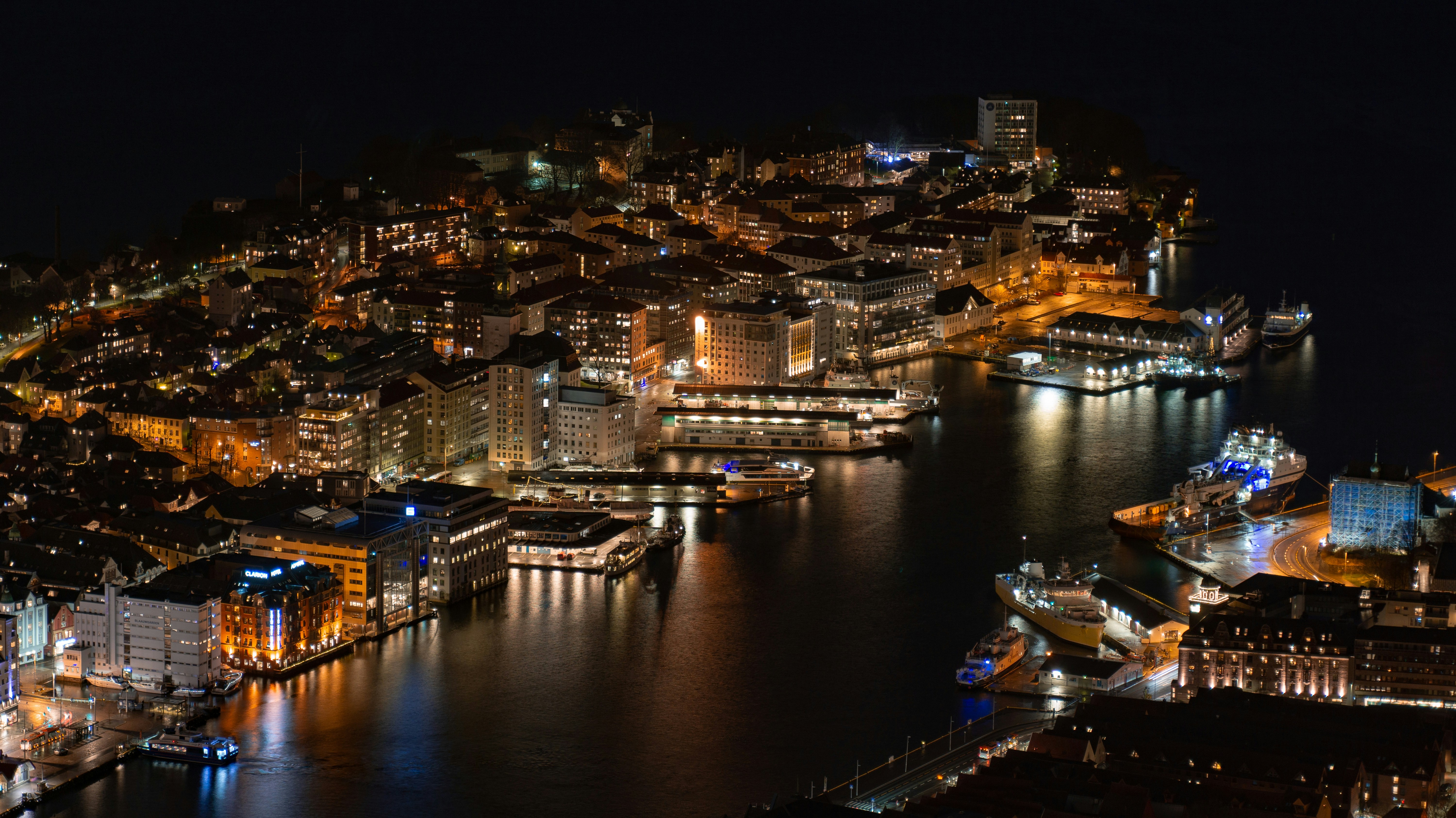 Night view of a cityscape with illuminated buildings and their reflections on calm water.