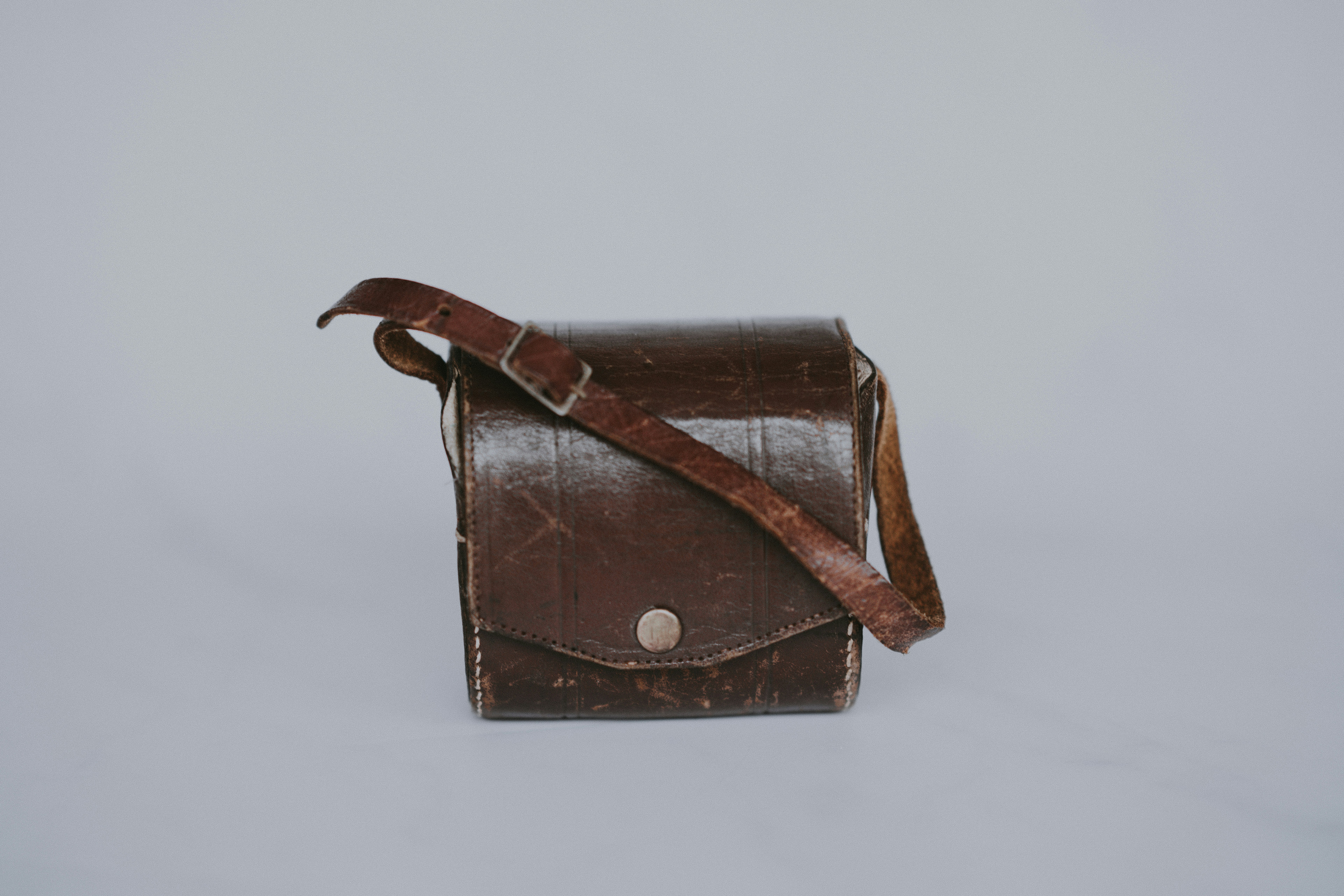 A vintage brown leather satchel with a sturdy strap, showcasing its worn texture and classic design.