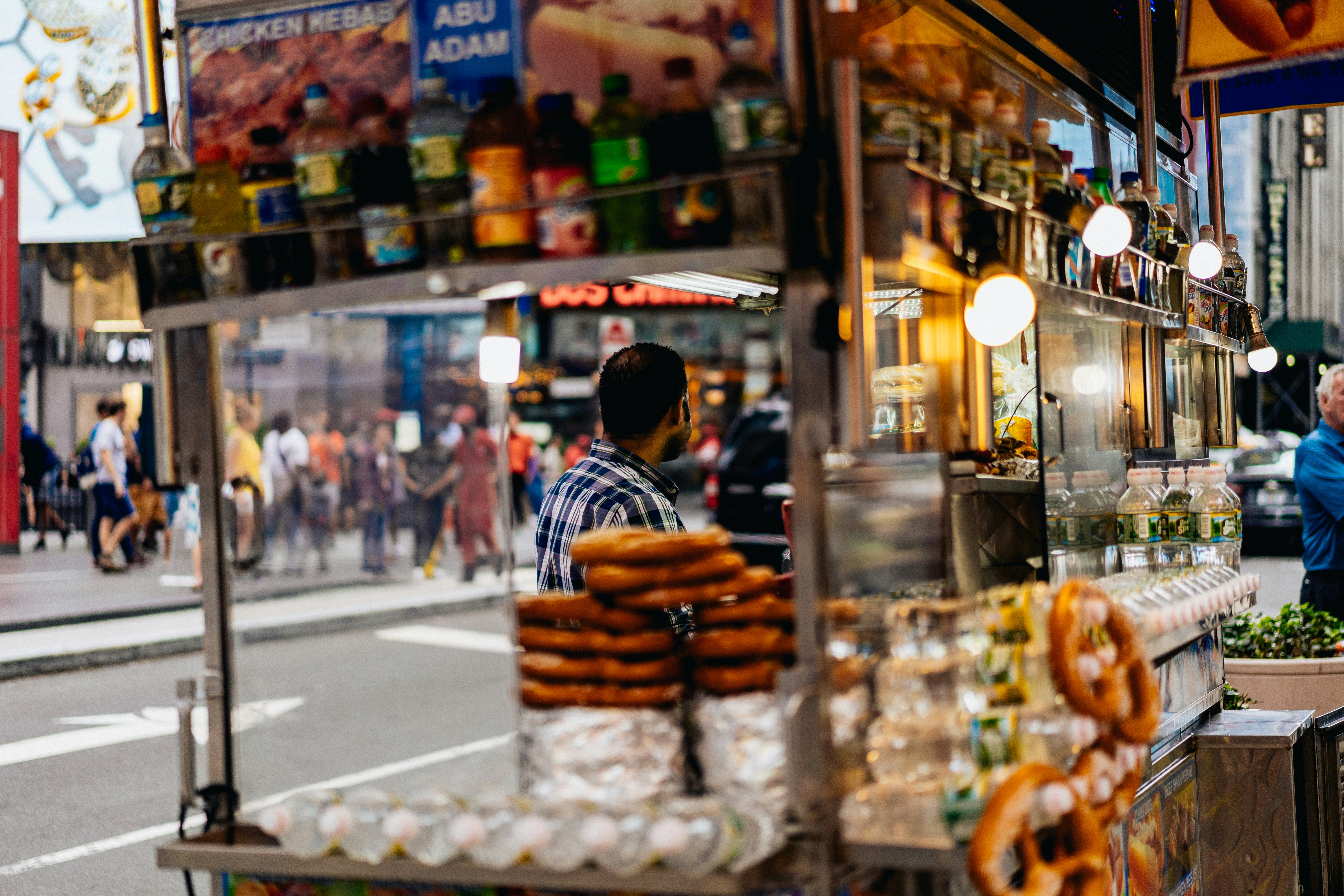 Street vendor cart with pretzels and drinks on a bustling city sidewalk.