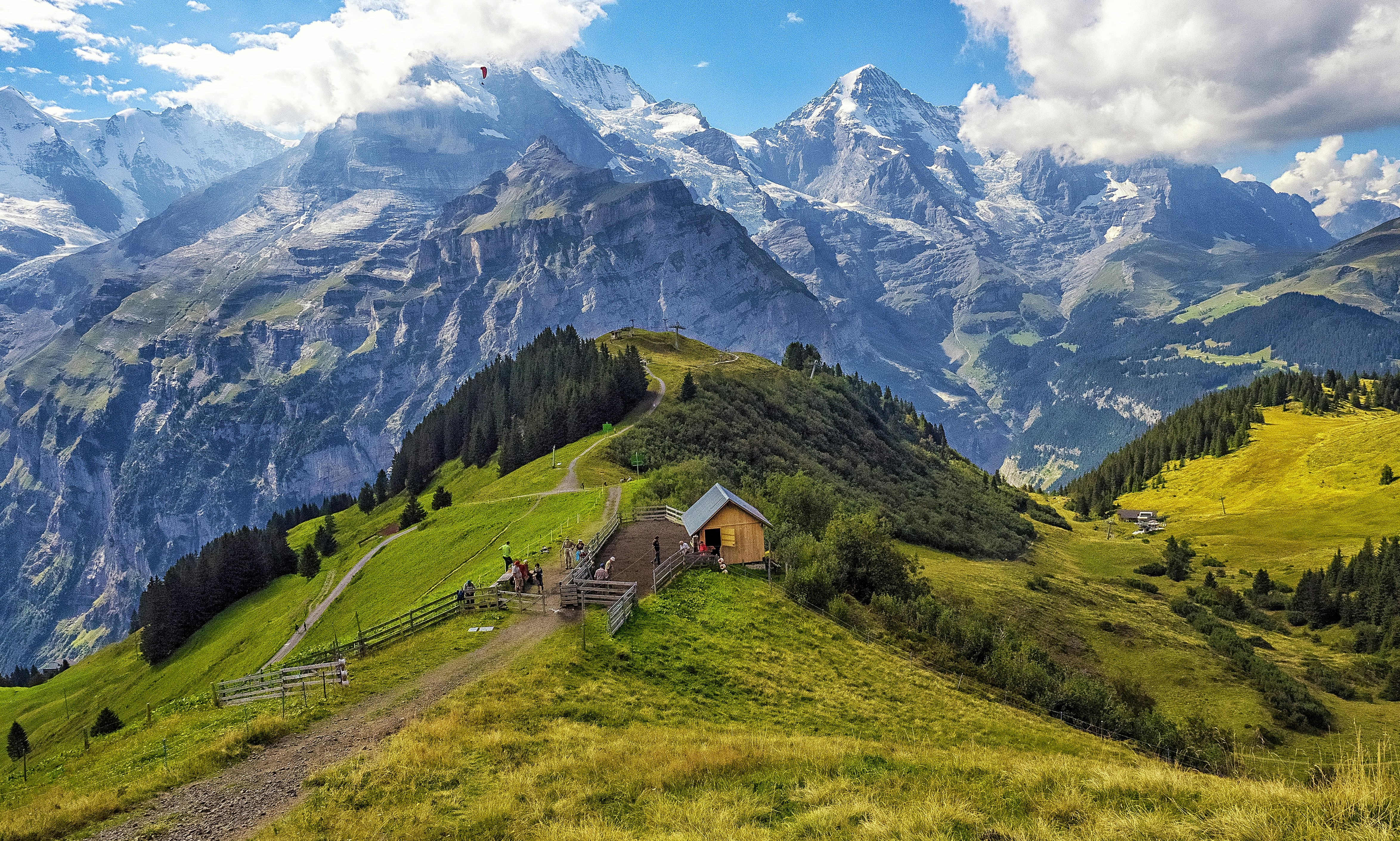 Charming wooden cabin nestled on a lush hillside, surrounded by majestic peaks and rolling green meadows.