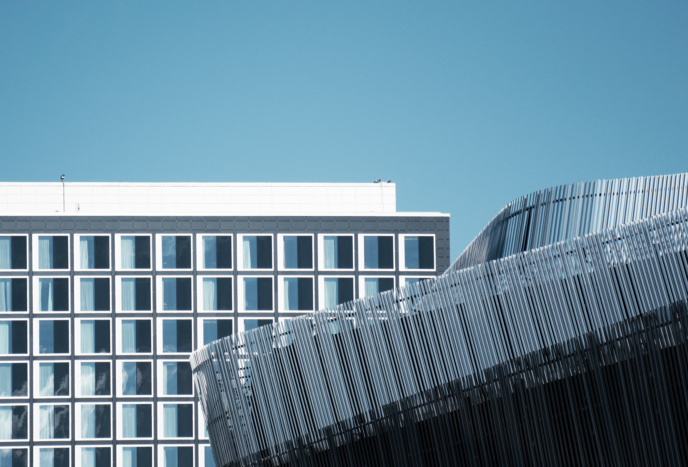 Modern buildings with grid and curved designs against a clear blue sky.