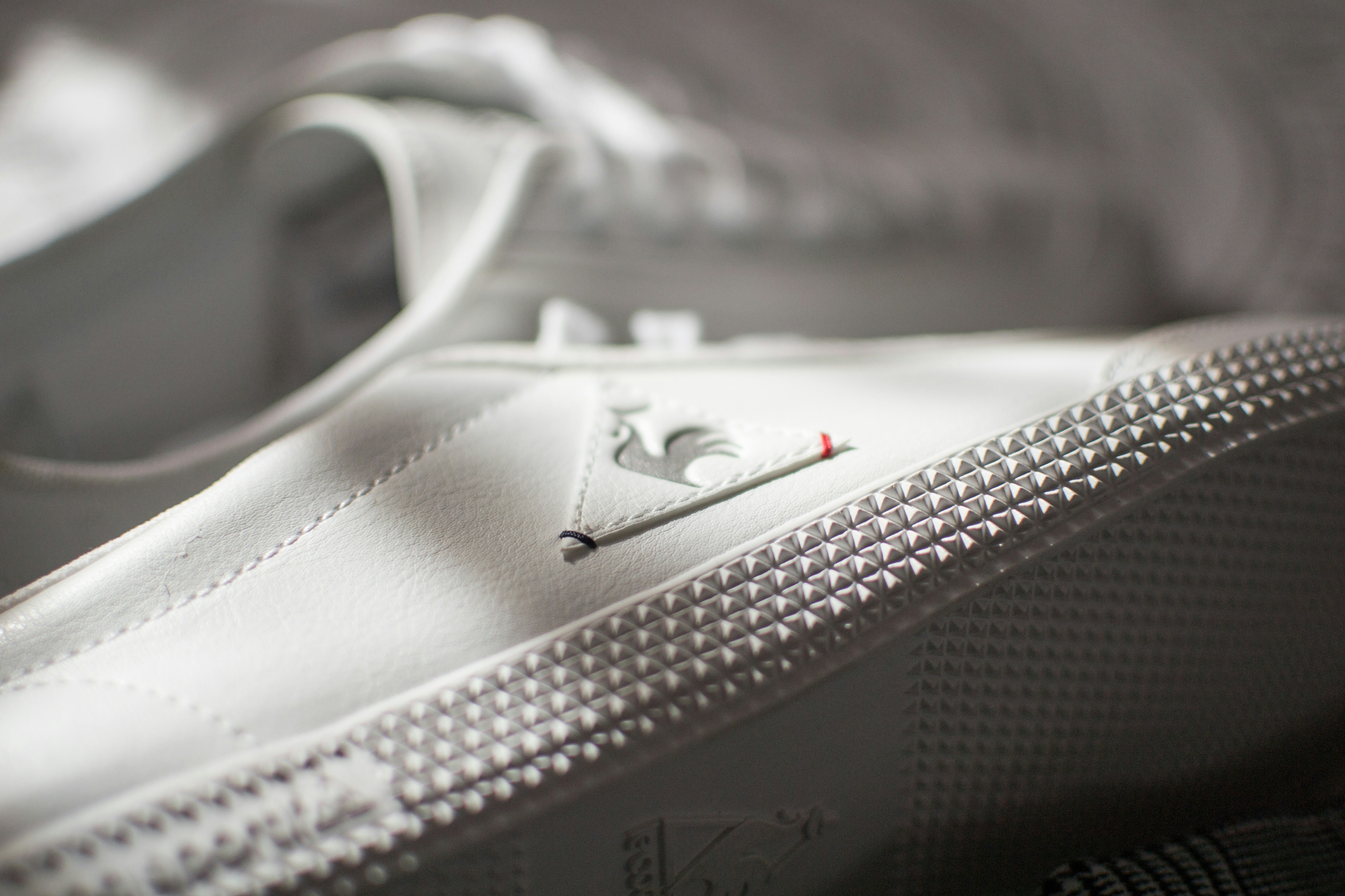 Close-up of a white sneaker with textured details and a distinct logo emblem.